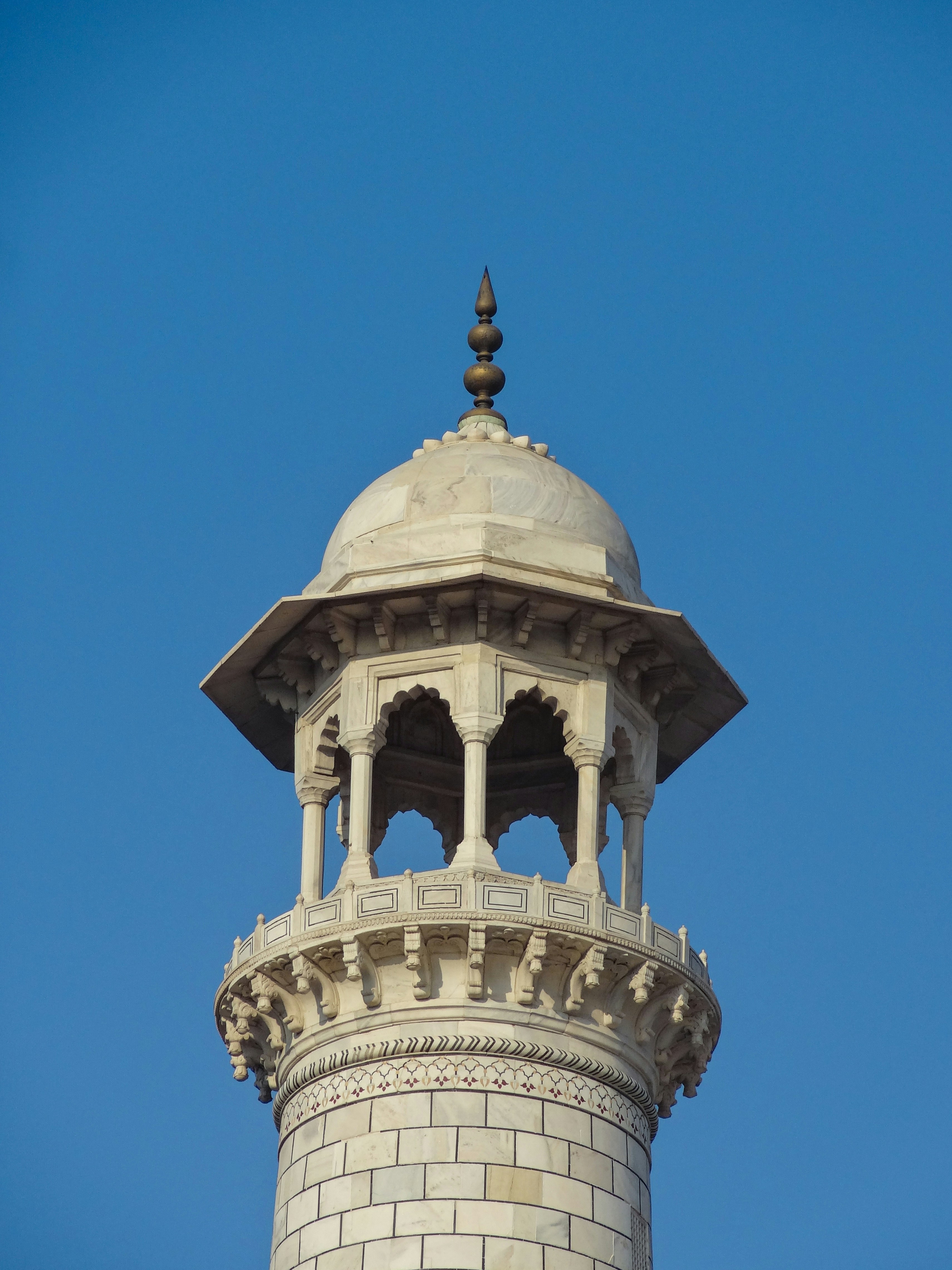 Photograph of a white marble minaret with ornate balconies rising against a clear cobalt blue sky.