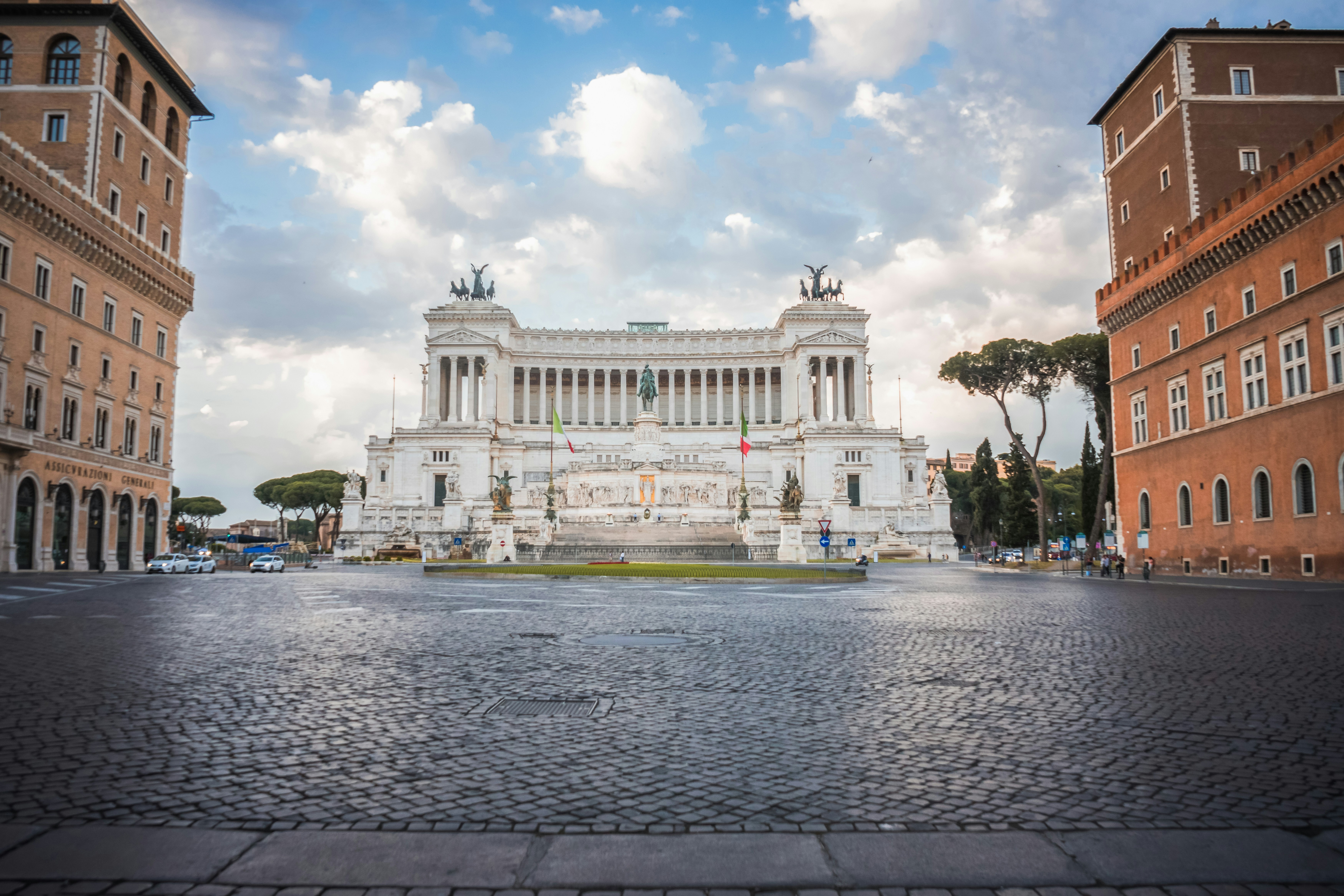 White neoclassical building framed by two red-brick structures under a cloudy sky.