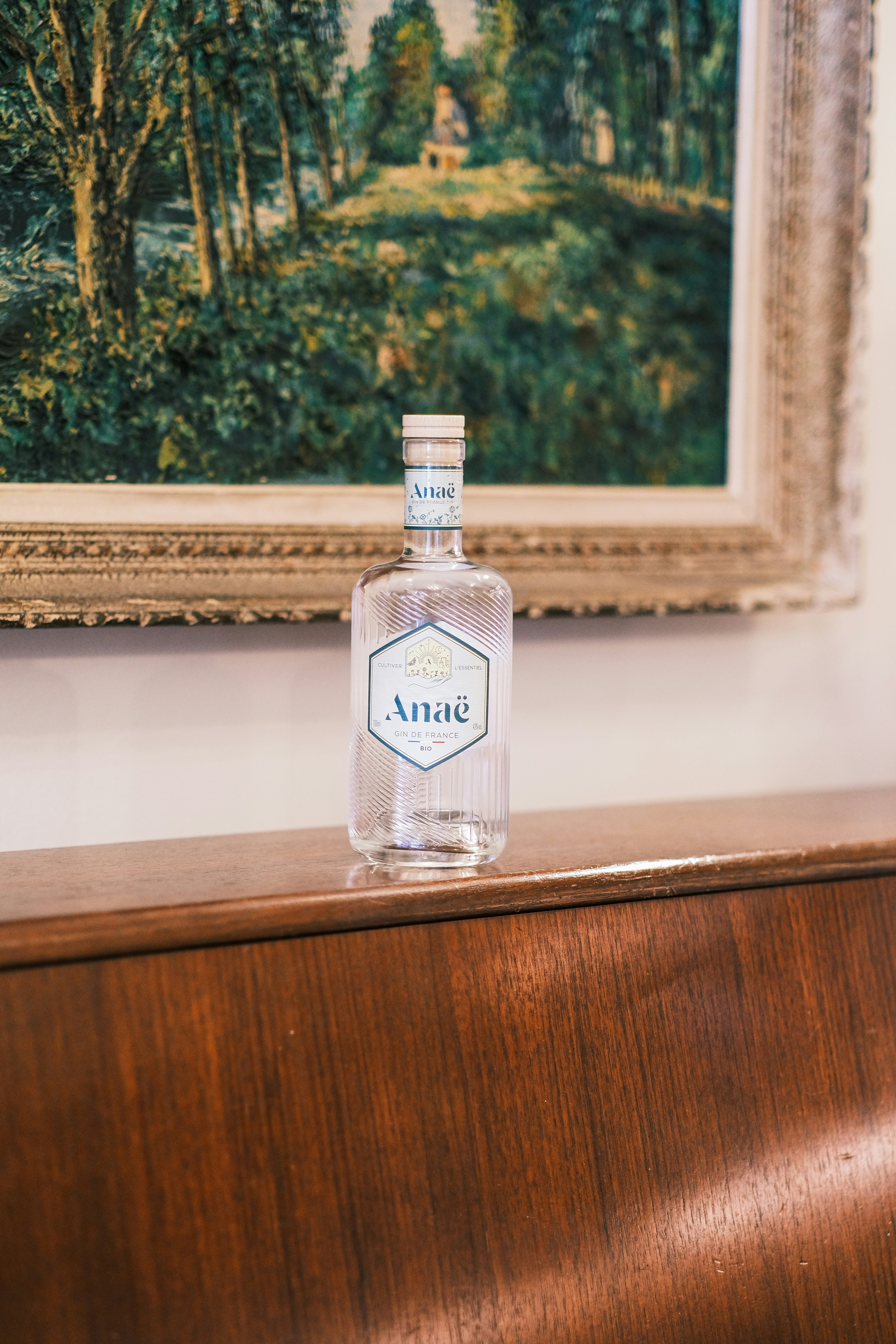Quiet Clarity: A Glass Bottle on Wood Under a Framed Landscape