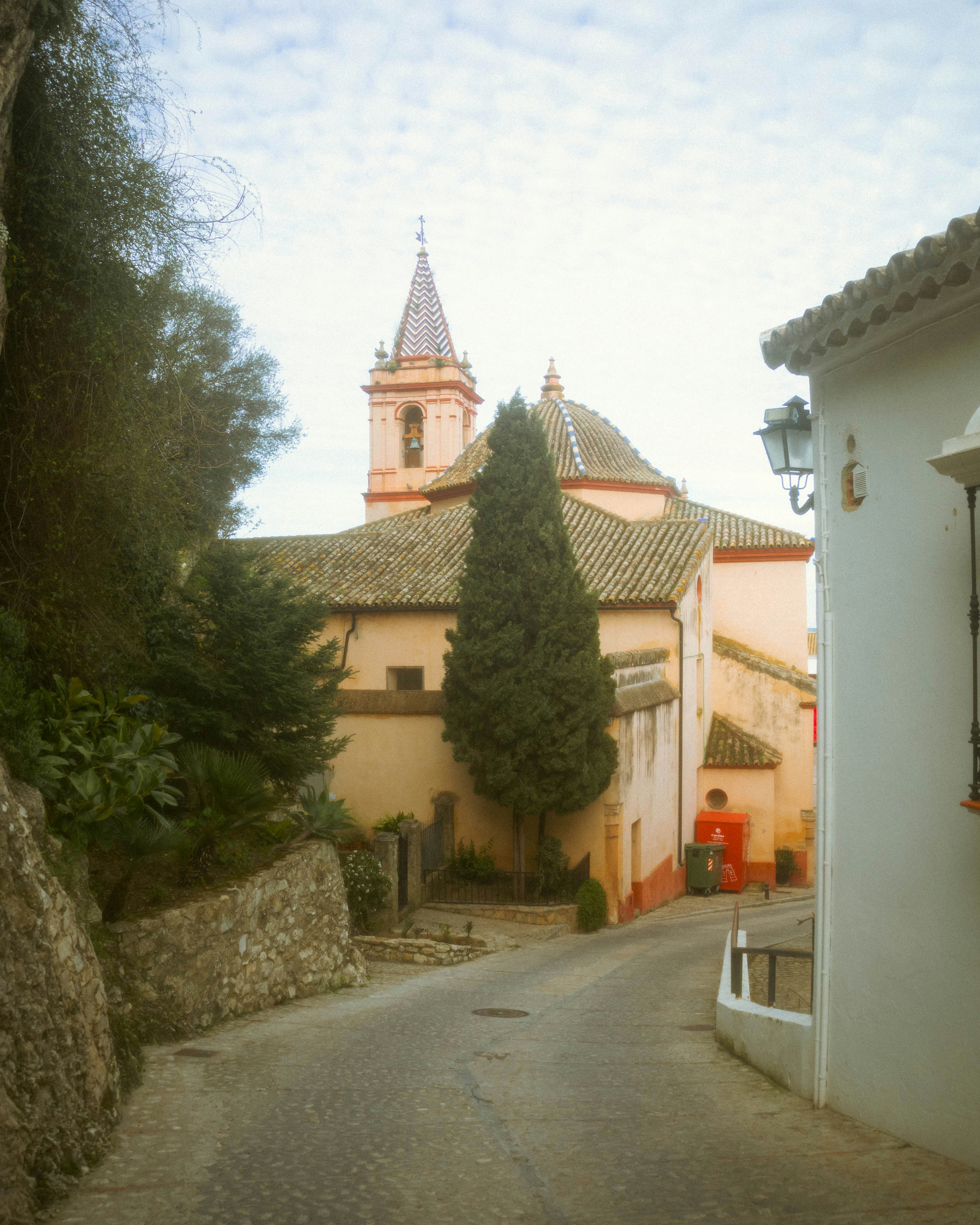 Toward the Spire: a sunlit village street converges on a pastel church with striped steeple