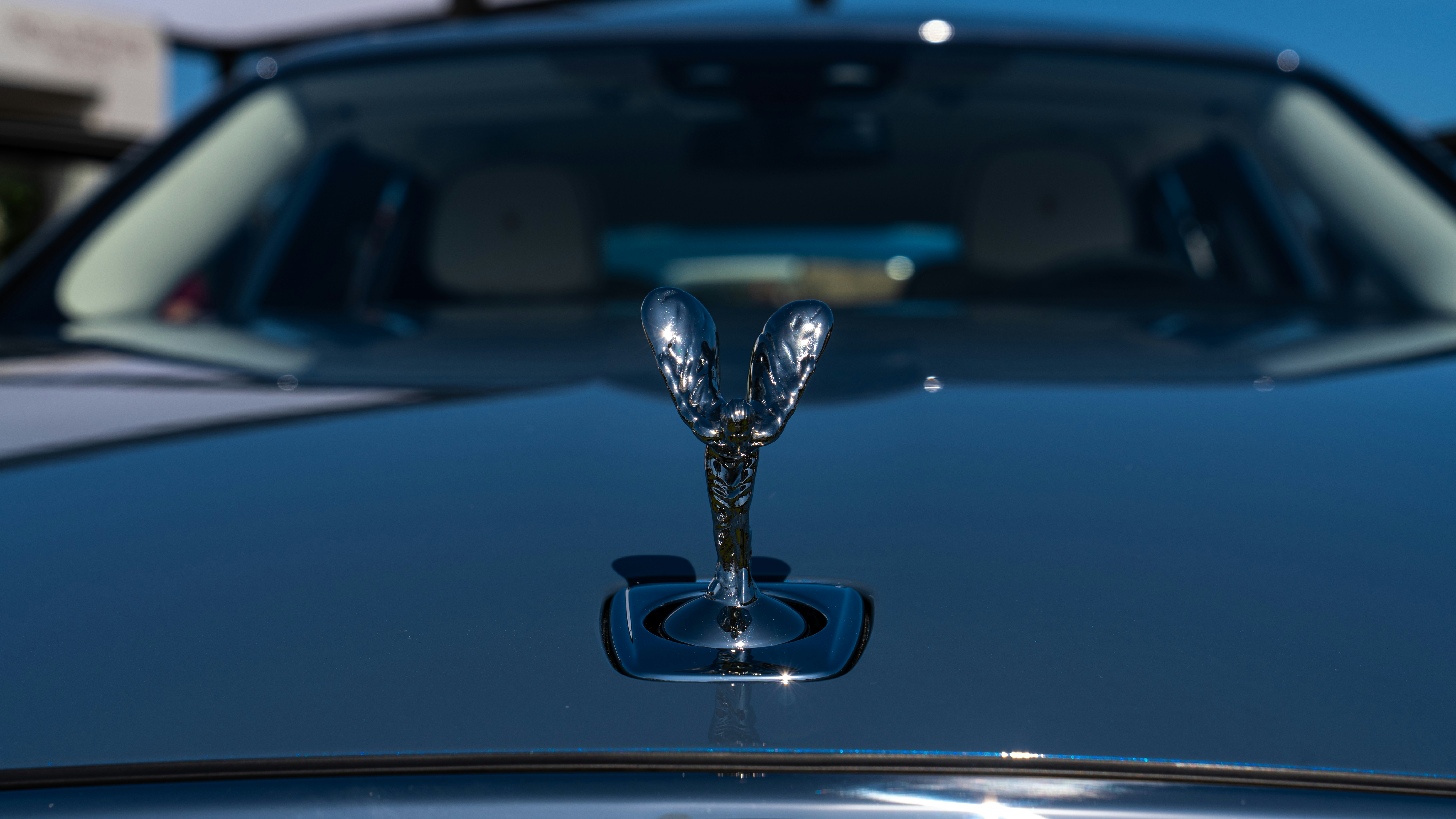Chrome Spirit: Close-Up of Rolls-Royce Hood Ornament on a Reflective Blue Hood