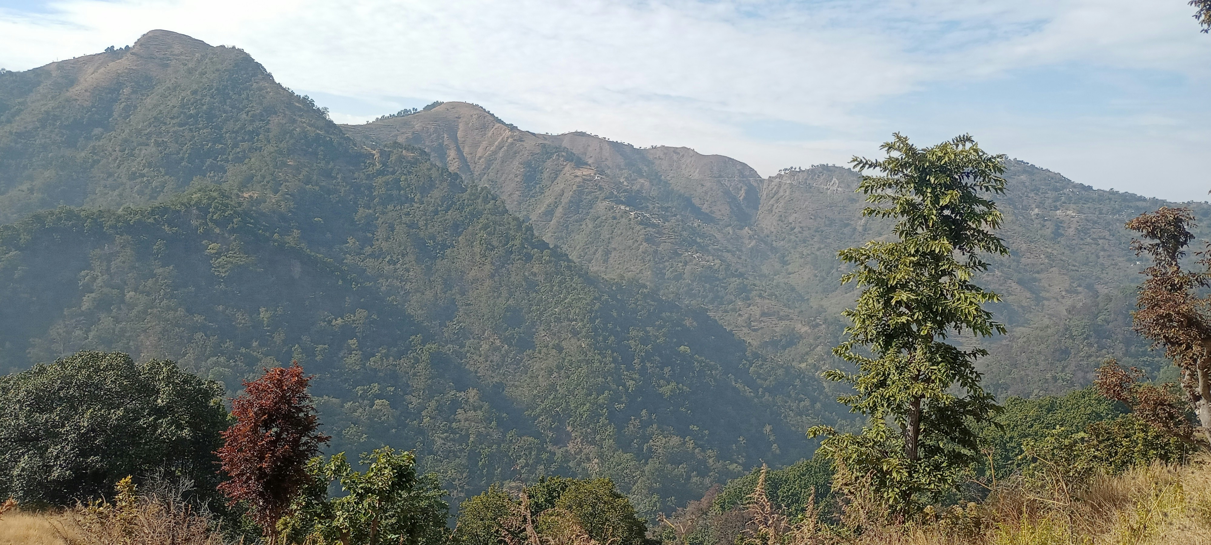 Lush green hills and rugged mountain peaks under a clear blue sky, showcasing the beauty of nature's untouched terrain.