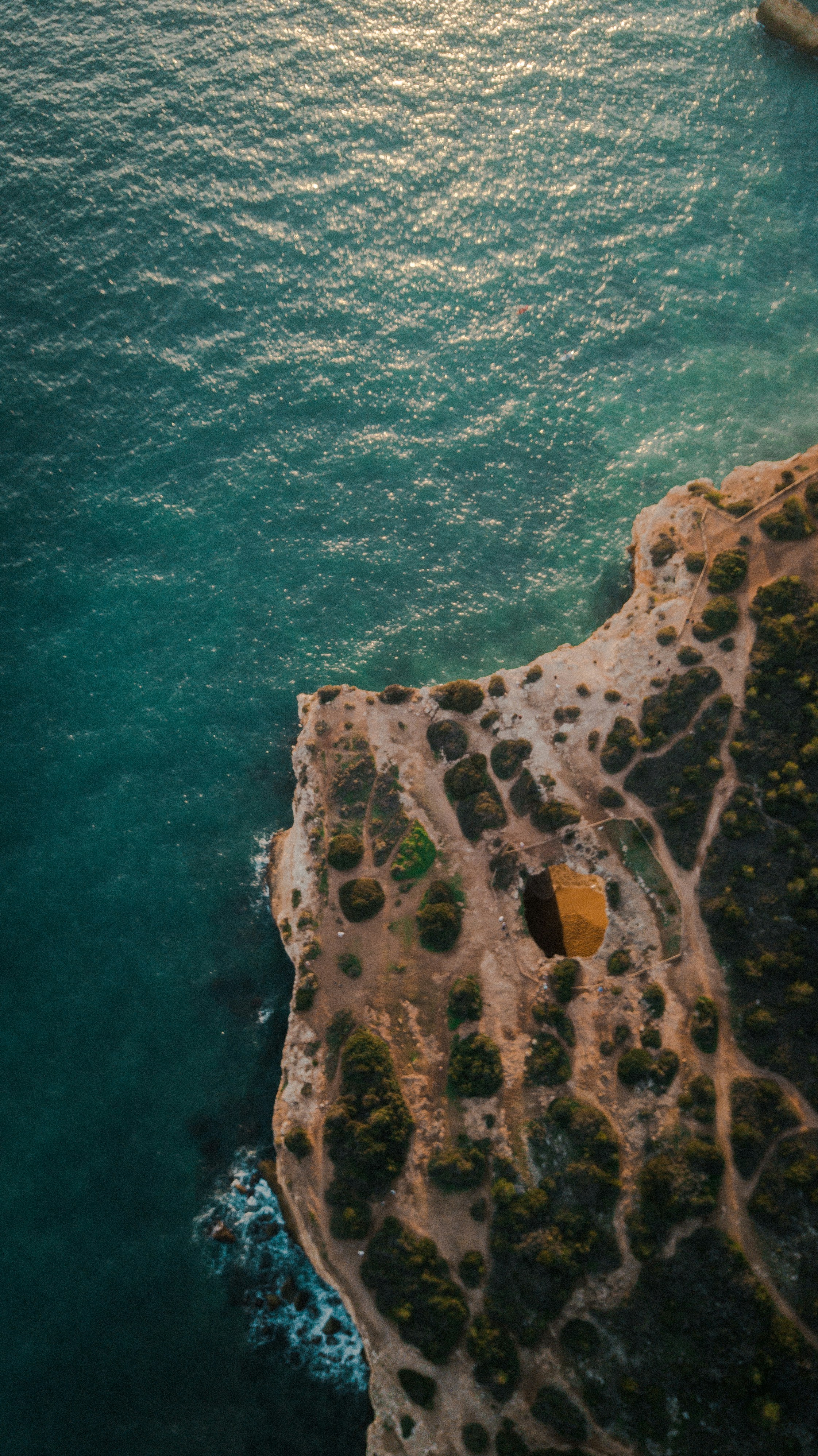 Aerial view of rugged coastline with turquoise waters meeting rocky cliffs at sunset.