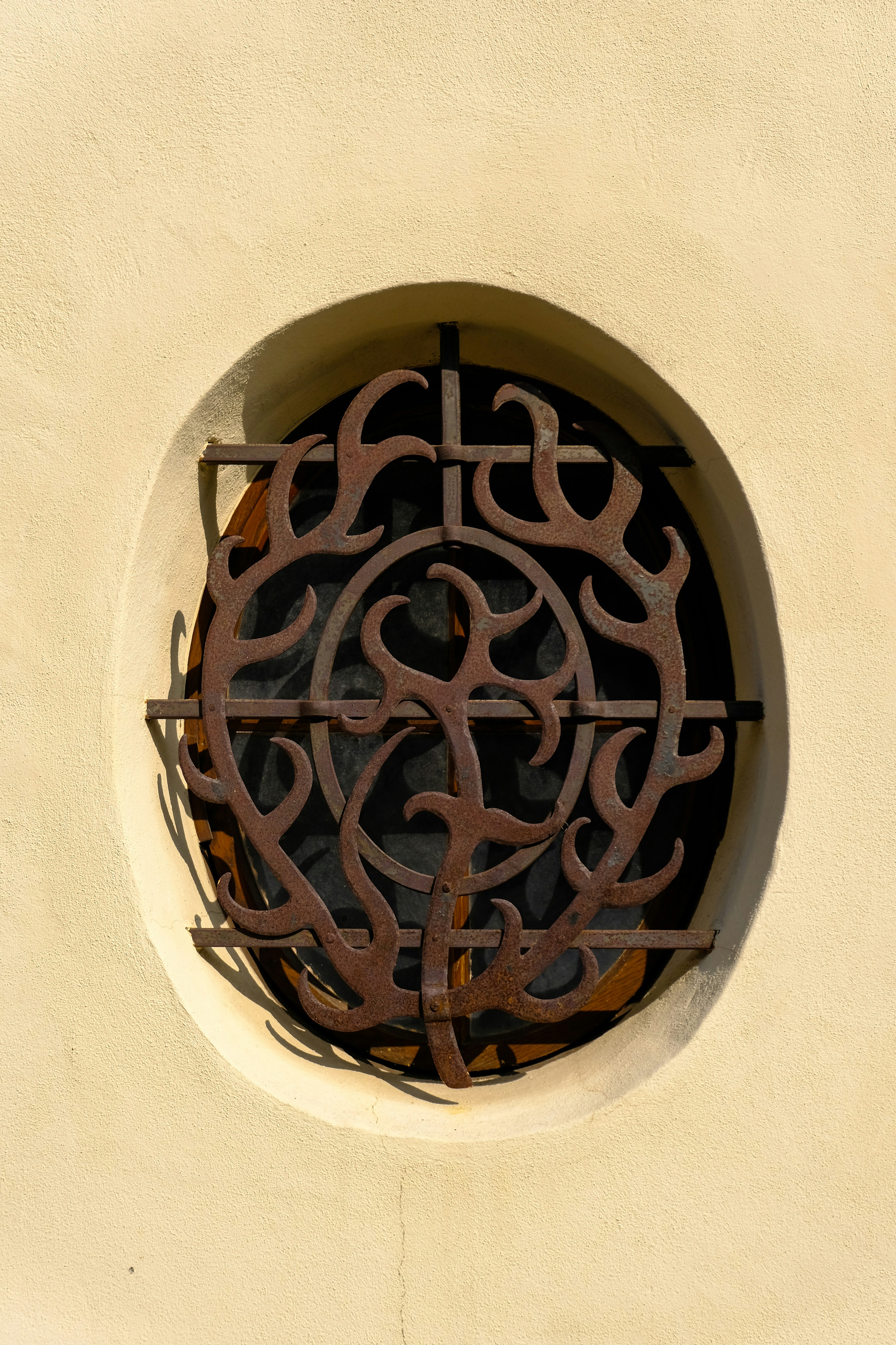 Sunlit Round Window: Rusted Iron Lattice in a Yellow Wall