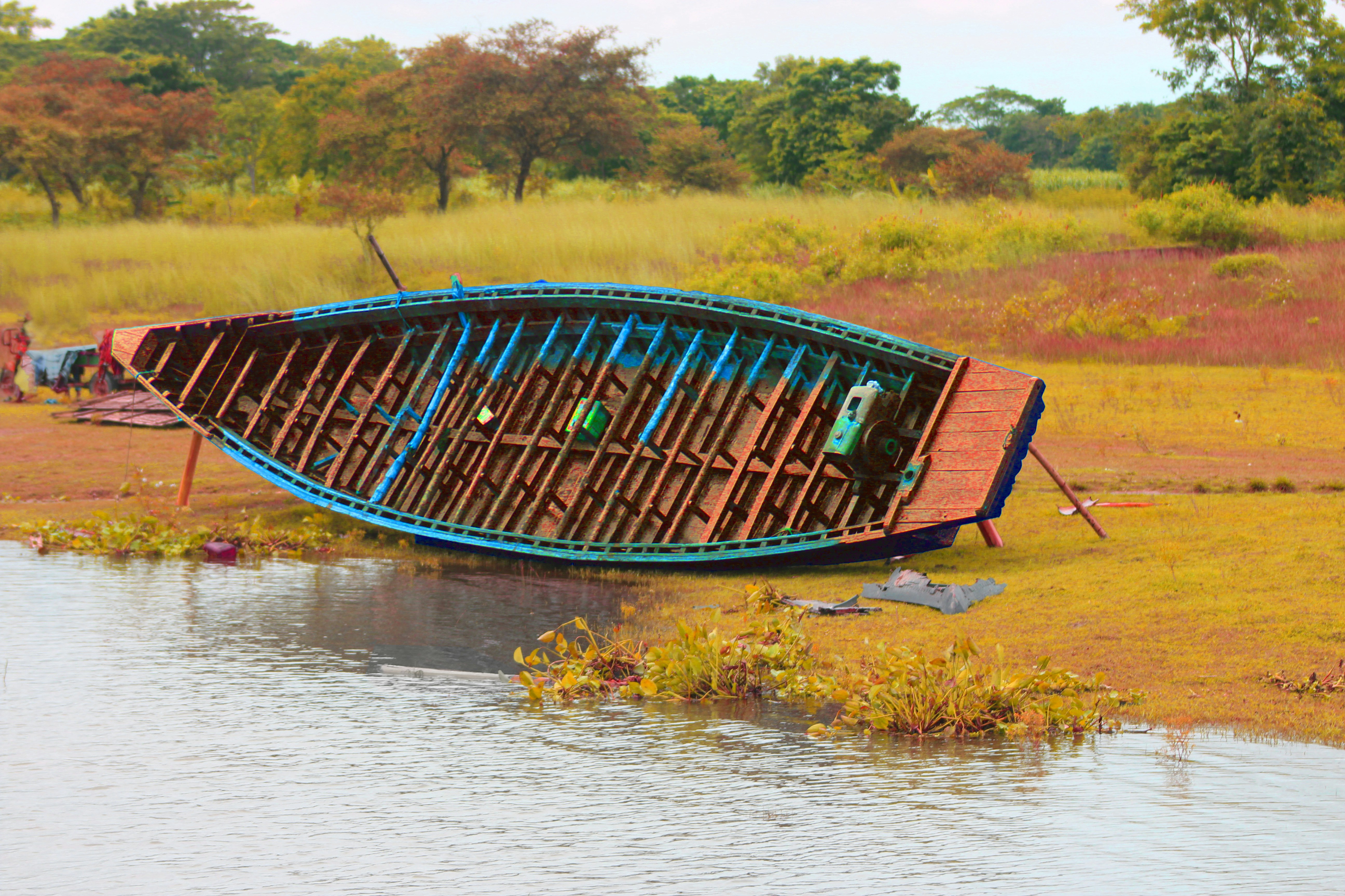 Beached turquoise-rimmed boat on a sunlit autumn riverbank