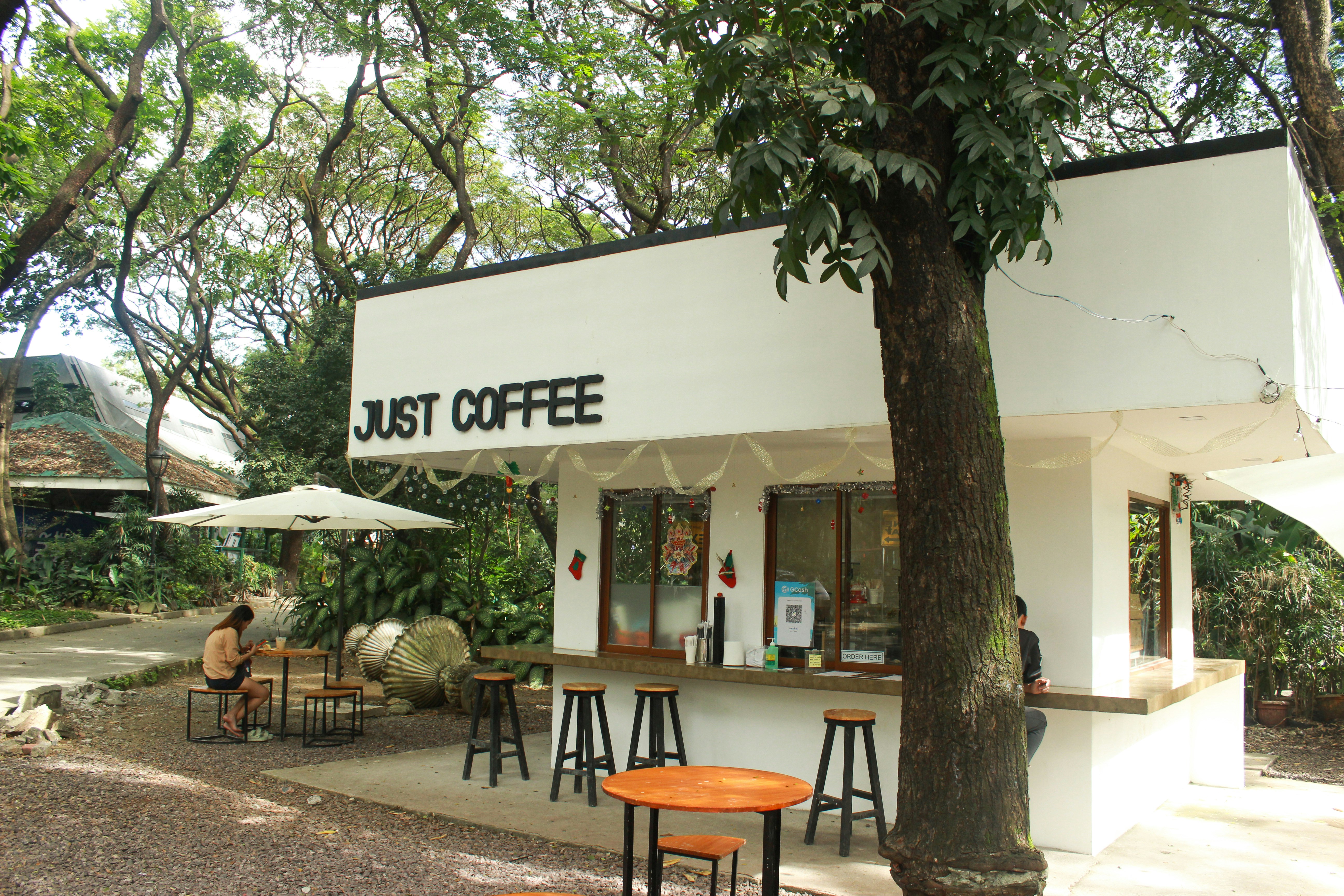 Outdoor cafe surrounded by lush trees and seating areas under umbrellas.