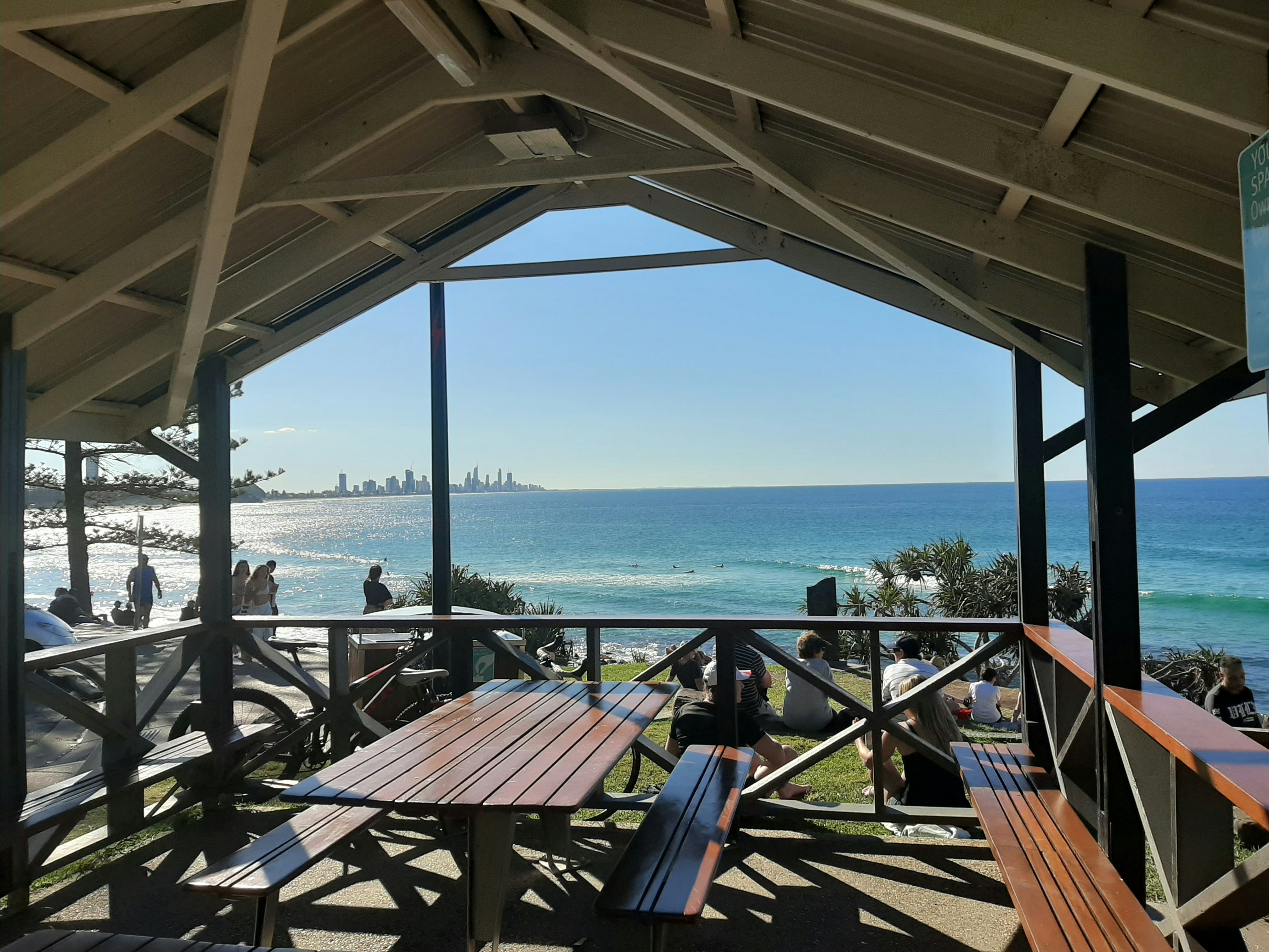 Beachfront pavilion overlooking the ocean with distant city skyline and sunlit waves. A gathering place for relaxation and enjoyment.