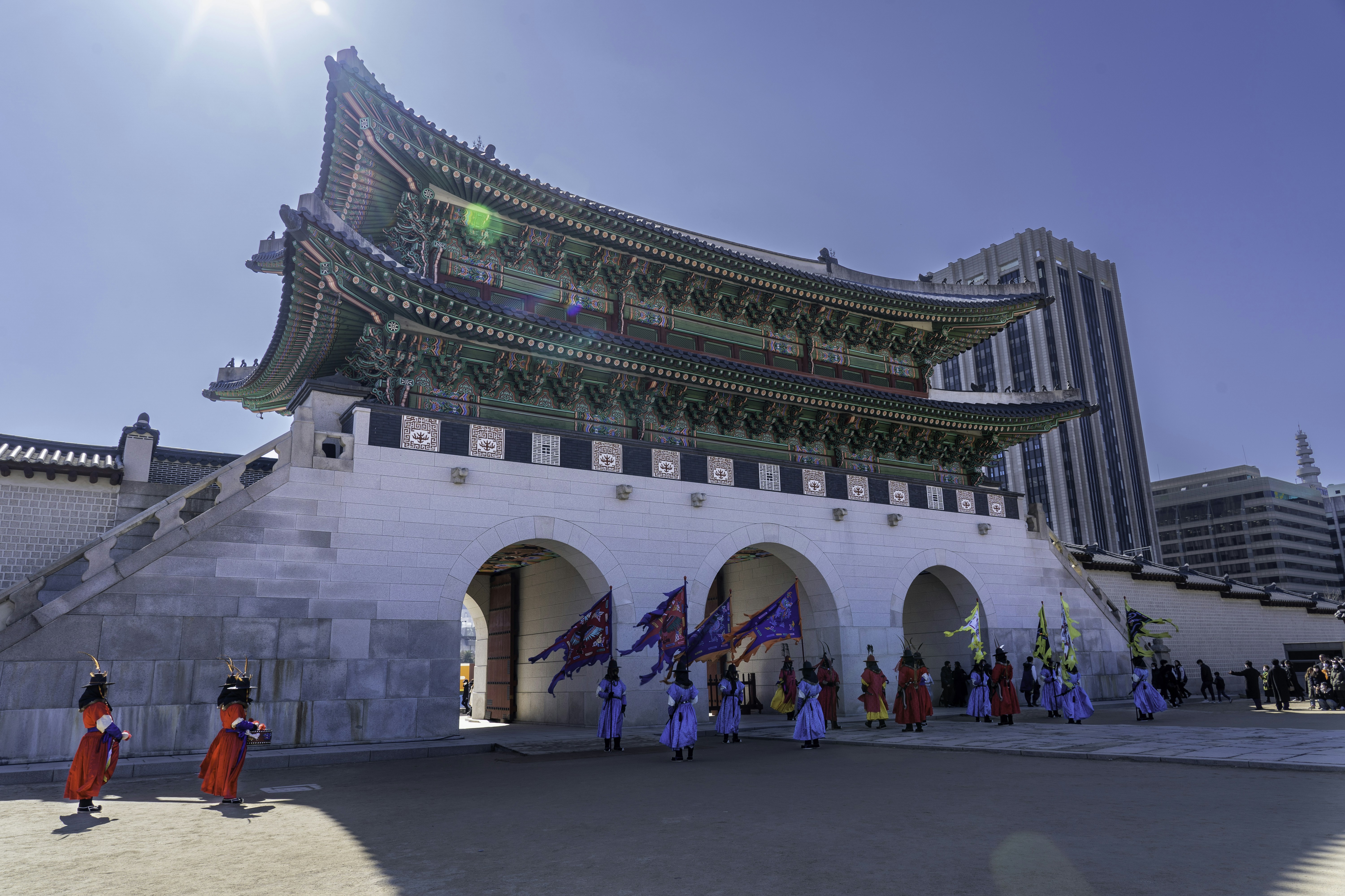 Traditional guards in vibrant attire stand before the historic Gwanghwamun Gate under a clear blue sky.