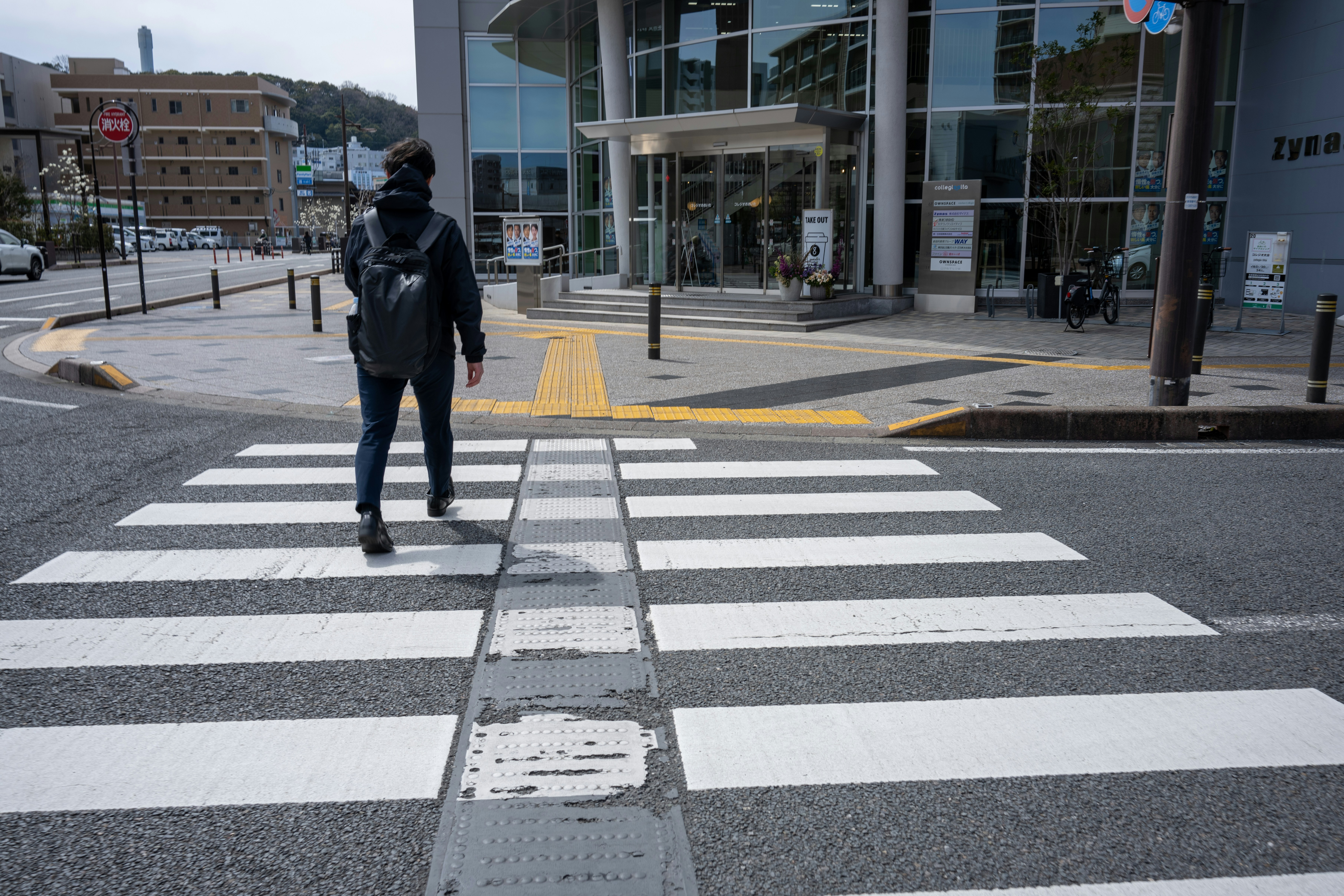 A man walking across a cross walk in front of a building photo – Free ...