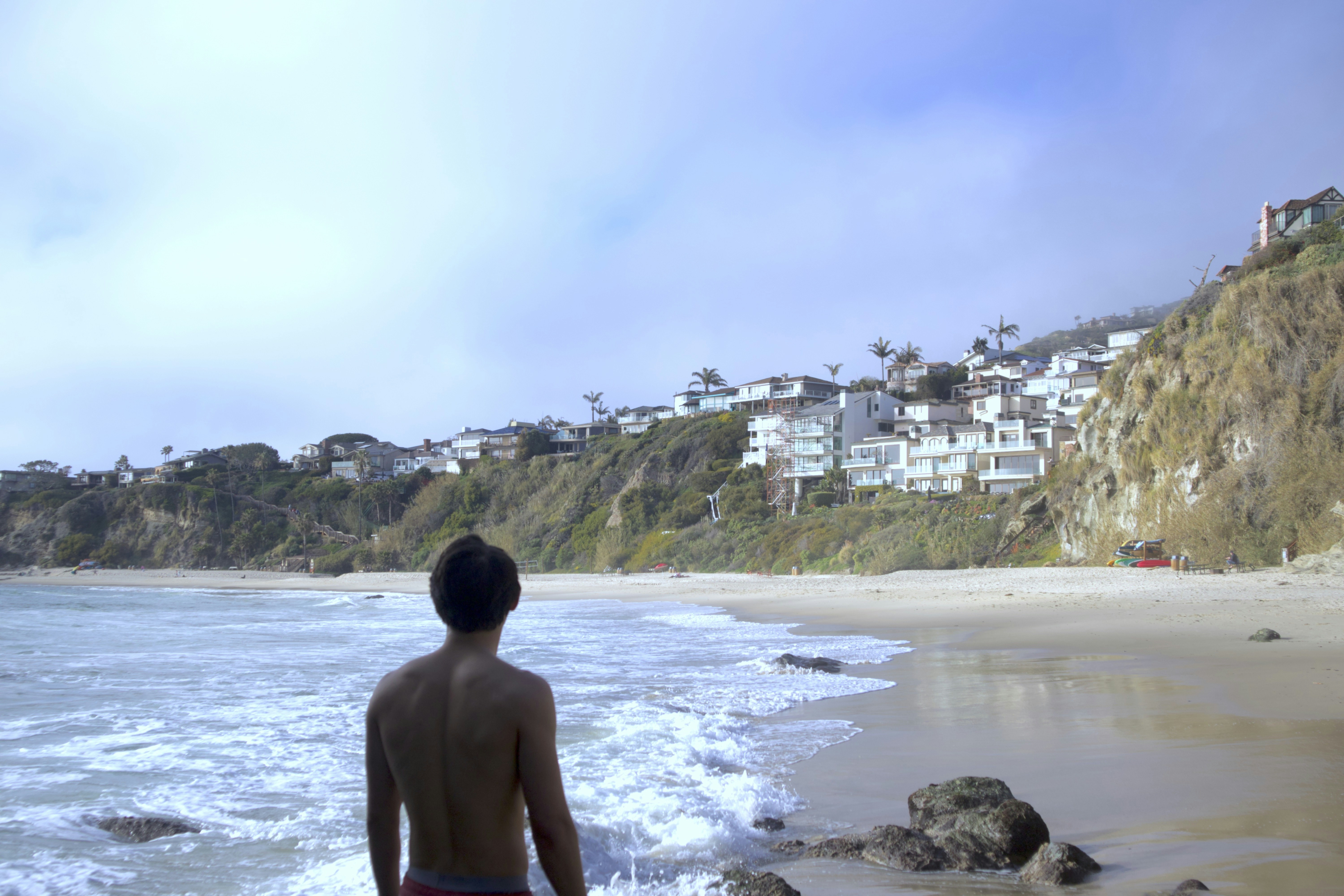 A man standing on top of a sandy beach next to the ocean photo – Free ...