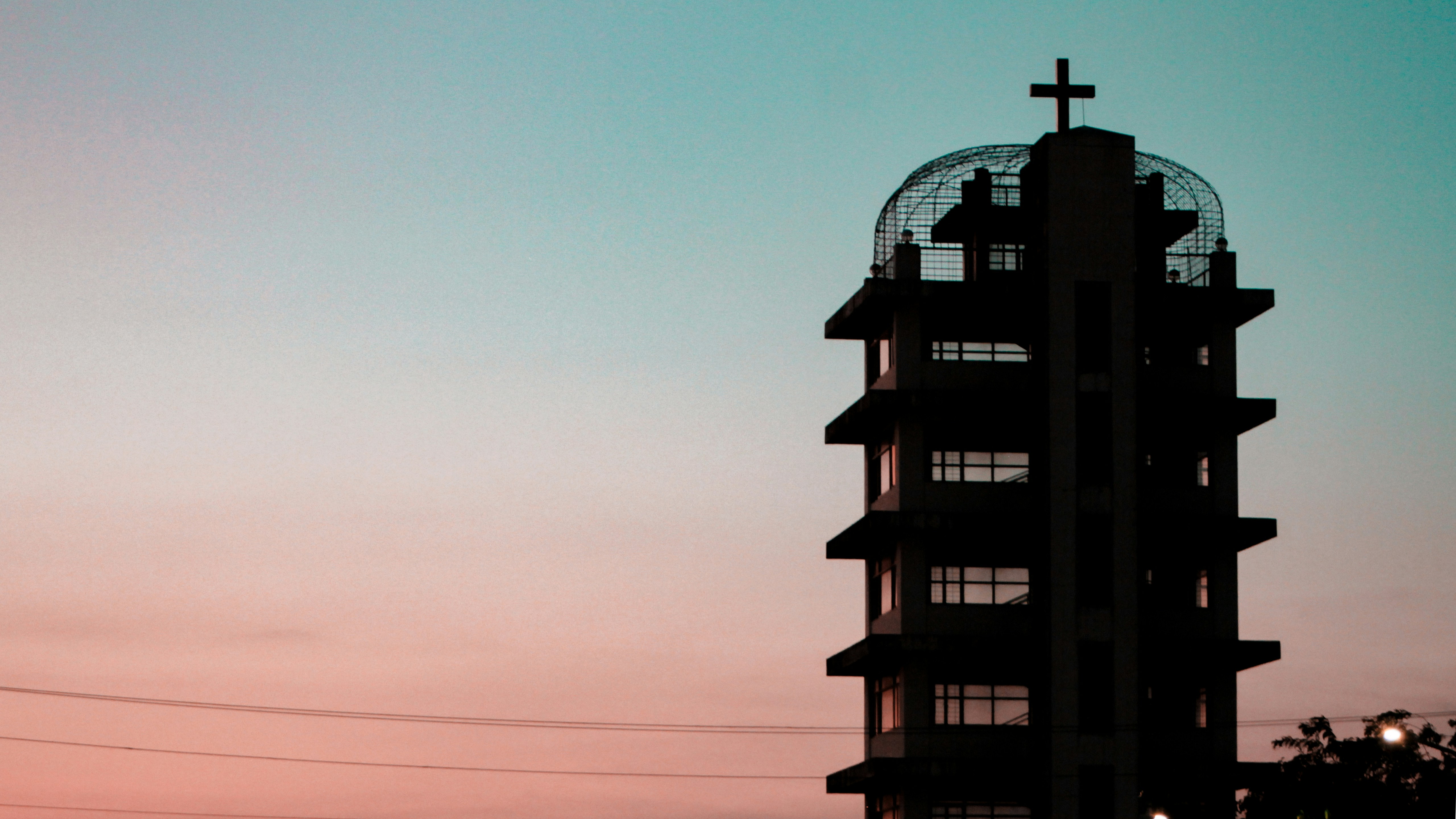 Towering structure with a cross at the top silhouetted against a gradient sky transitioning from blue to pink.