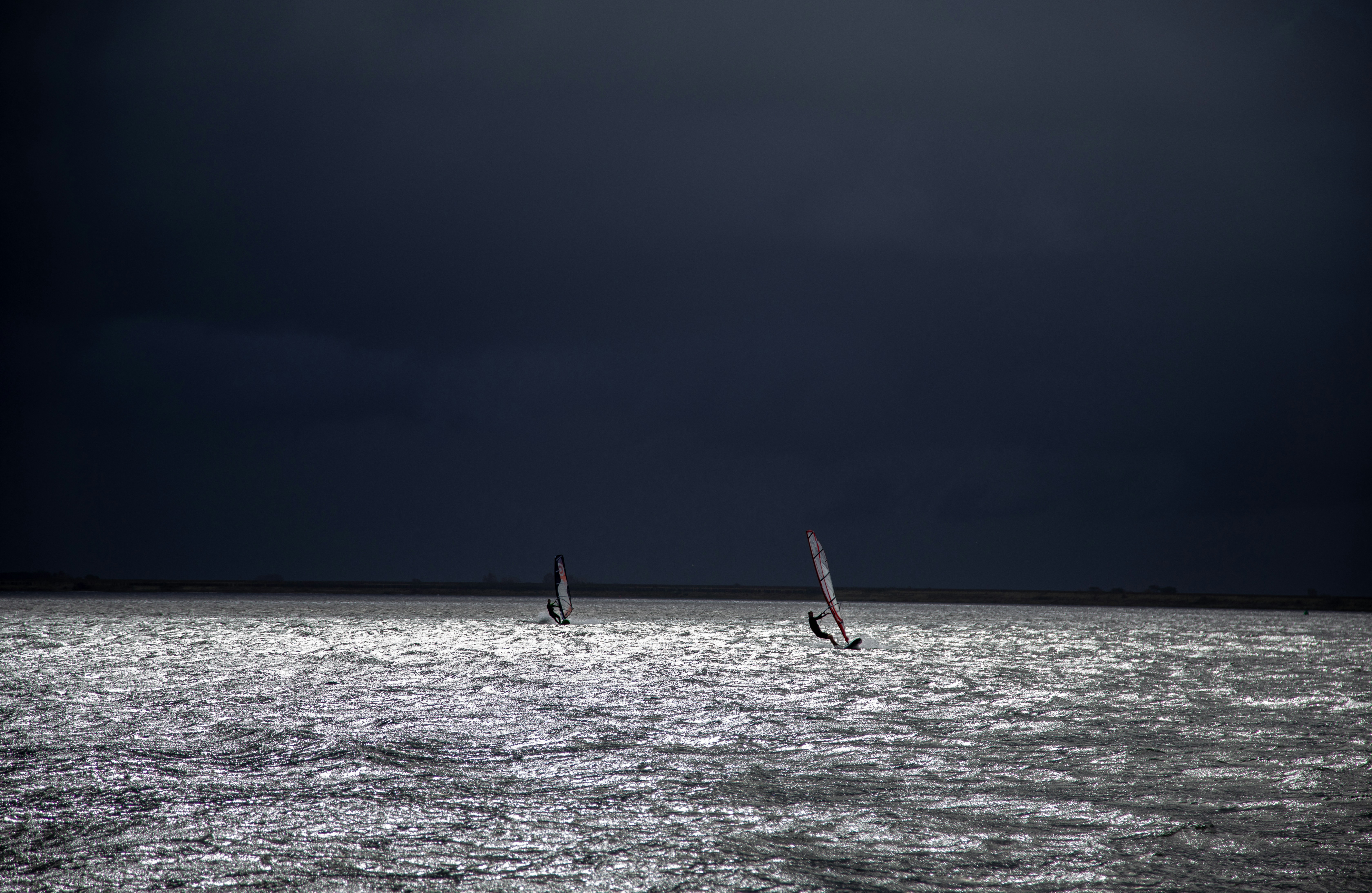 Two windsurfers in the ocean under a dark sky photo – Free ...