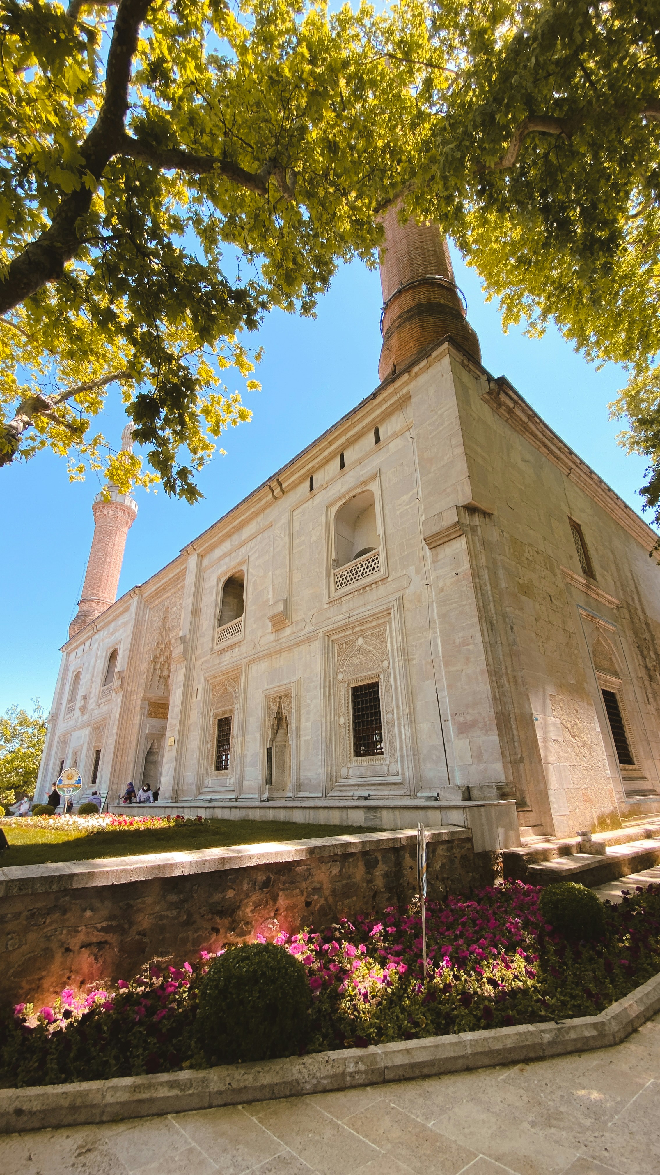Sunlit Marble Facade under a Canopy of Green: Twin Minarets Frame a Historic Mosque