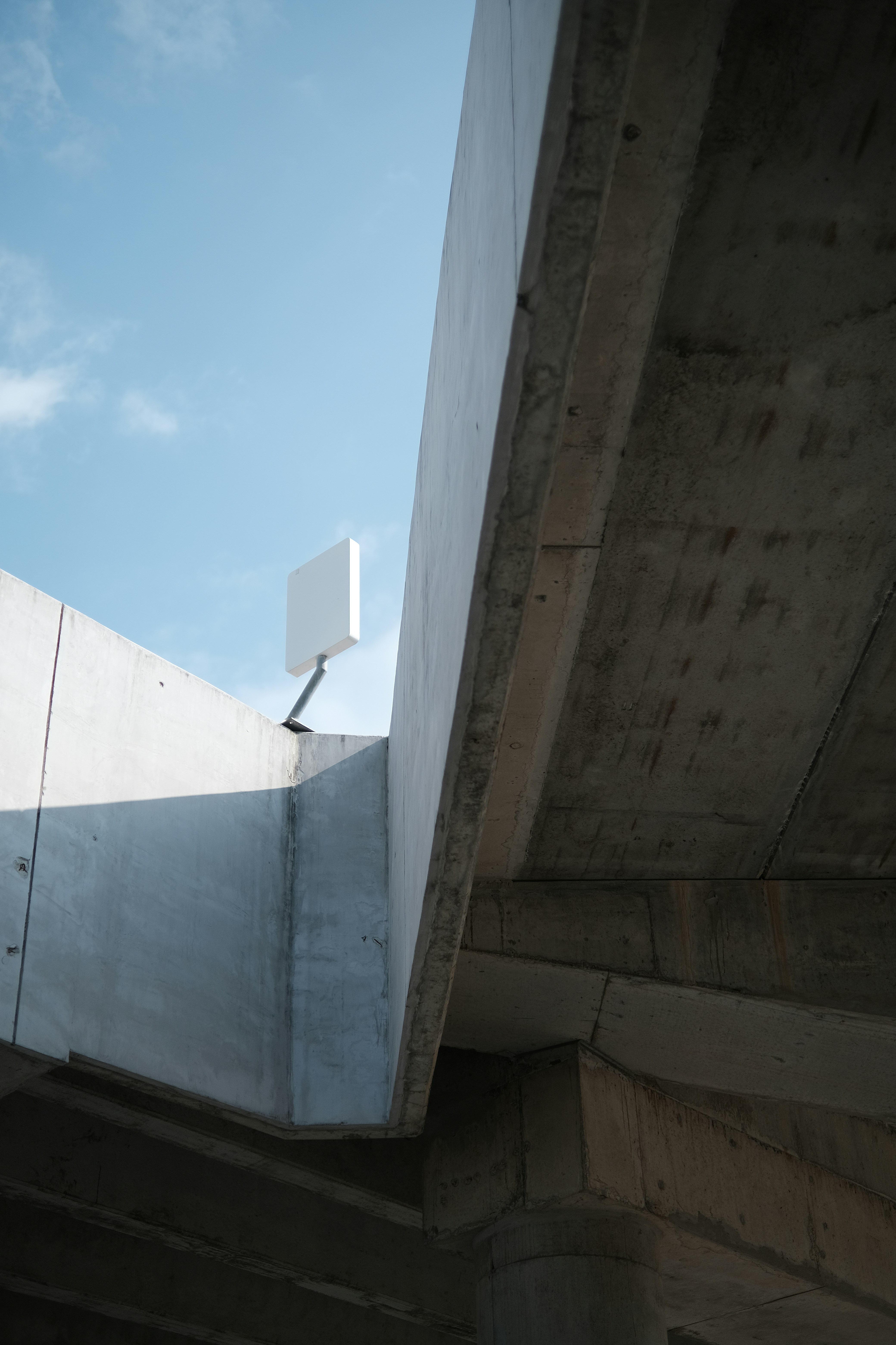 A minimalist view of concrete architecture framed by a clear blue sky, featuring a white antenna emerging from the structure.