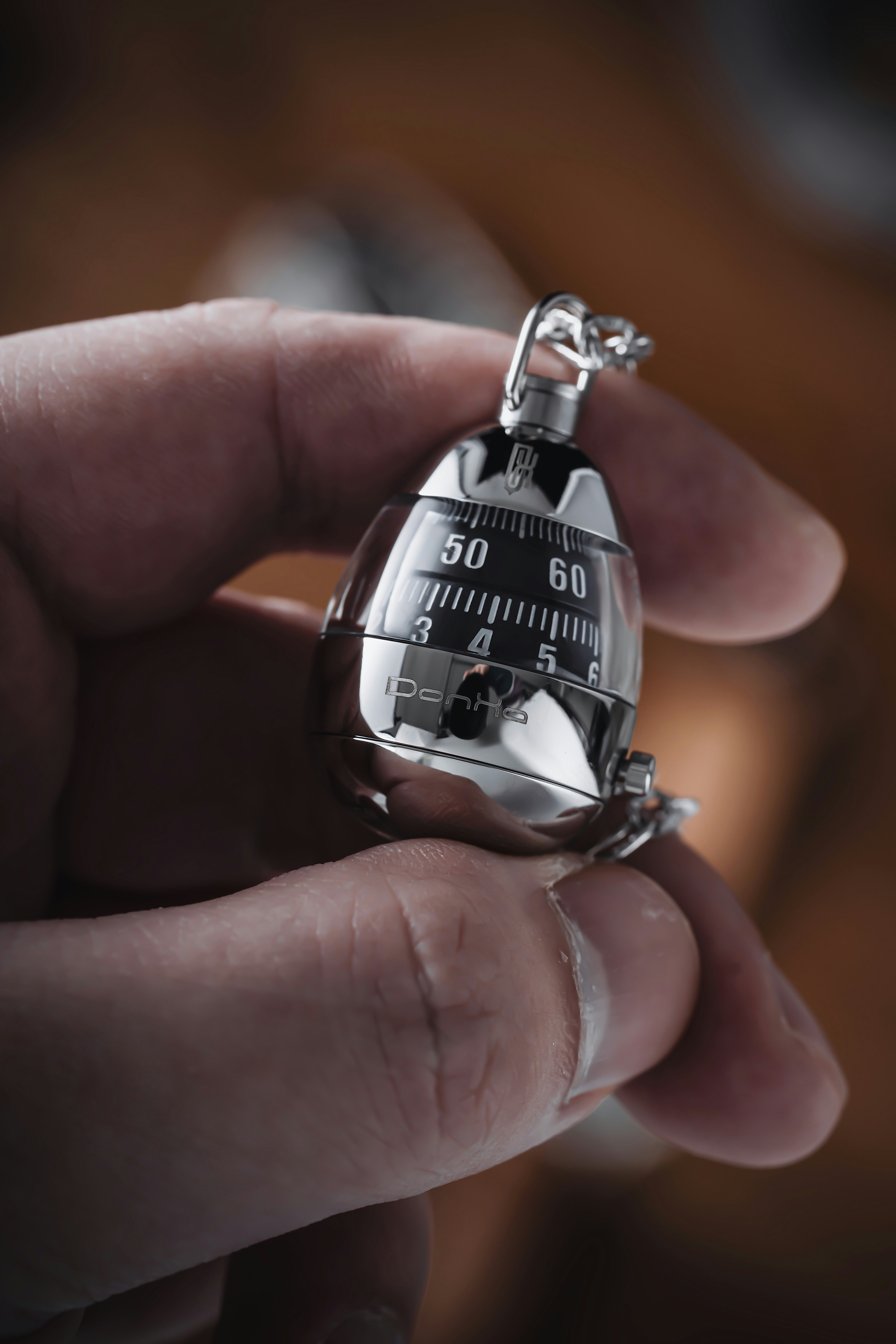 Close-up of a sleek, metallic timer held in a hand, showcasing its detailed dial and polished finish.