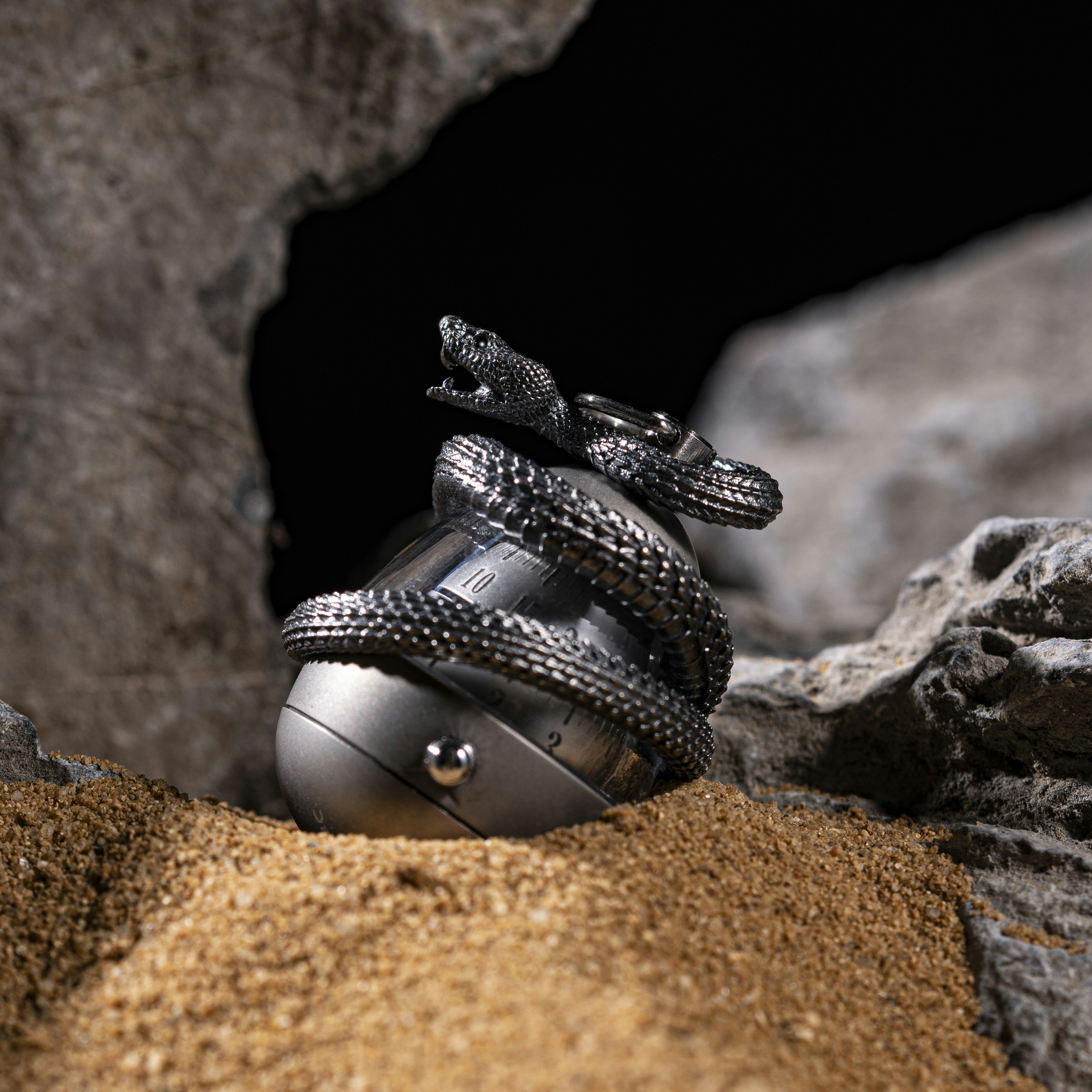 Guarded Coil: A Snake-Wrapped Lens Cap in Sand by a Cave Entrance