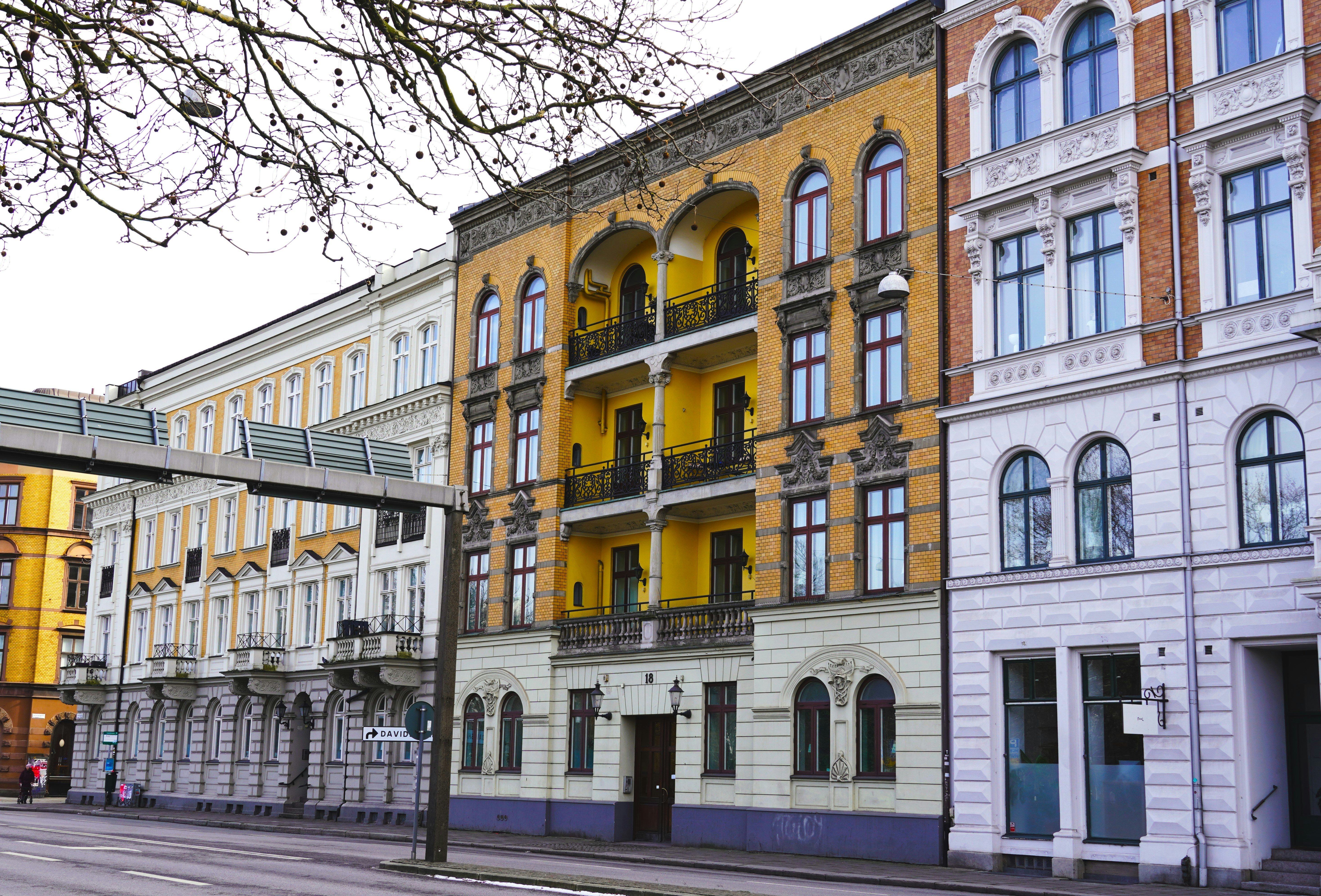 A vibrant yellow balcony contrasts with the muted tones of neighboring buildings along a city street, showcasing diverse architectural influences.