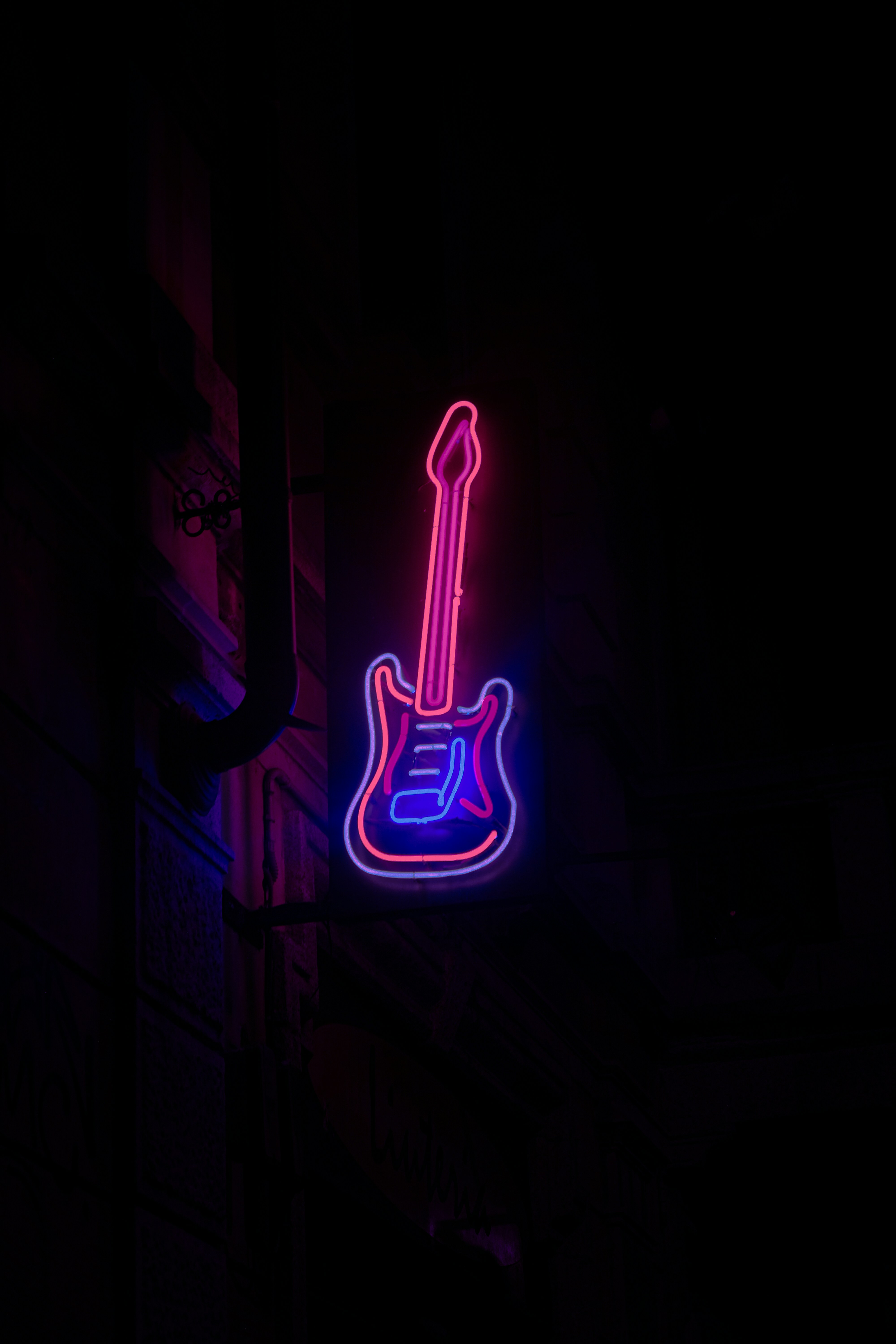 A neon guitar sign hanging from the side of a building photo – Free ...