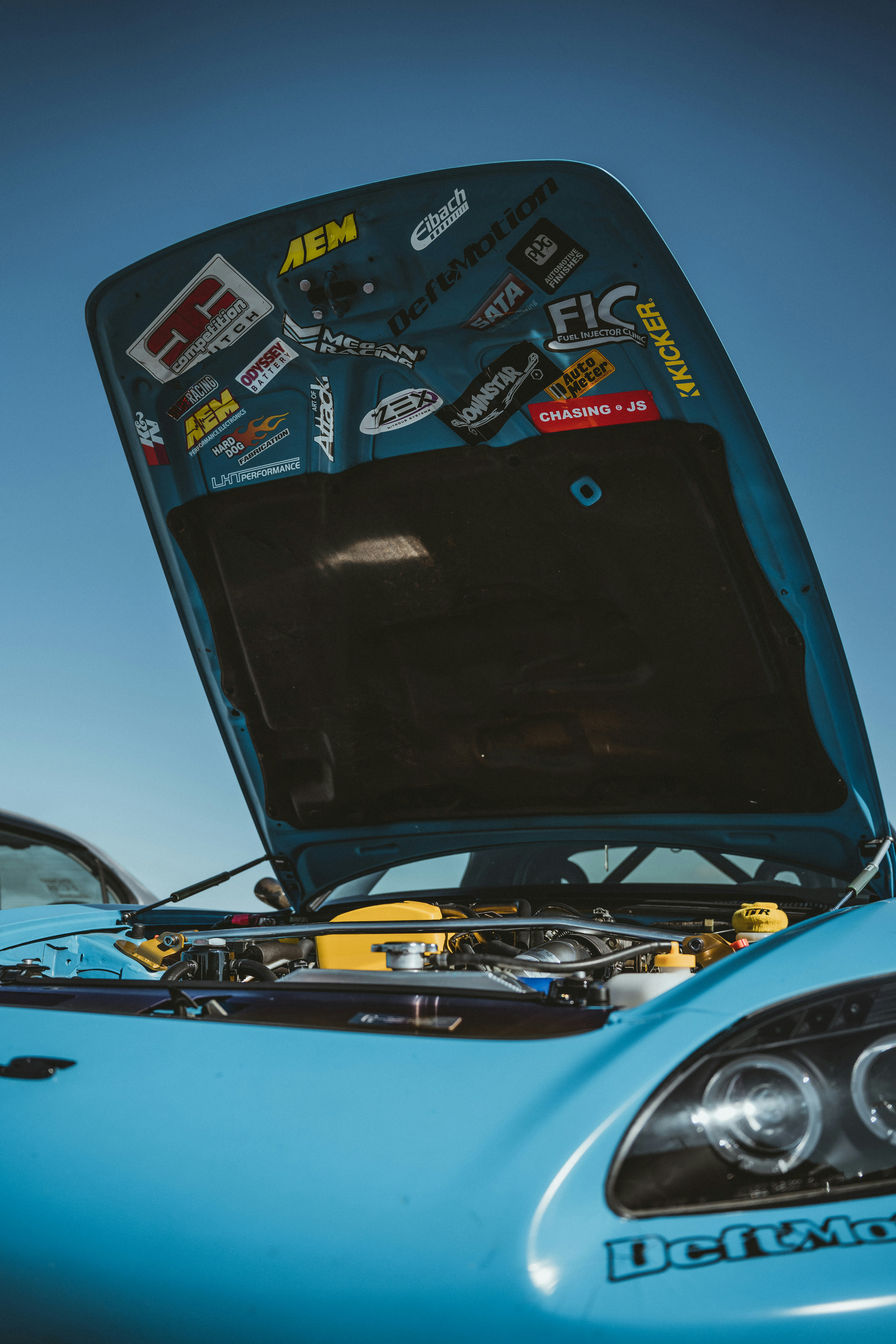 Stickered Blue Racer: Engine Bay Uncovered Under an Open Hood