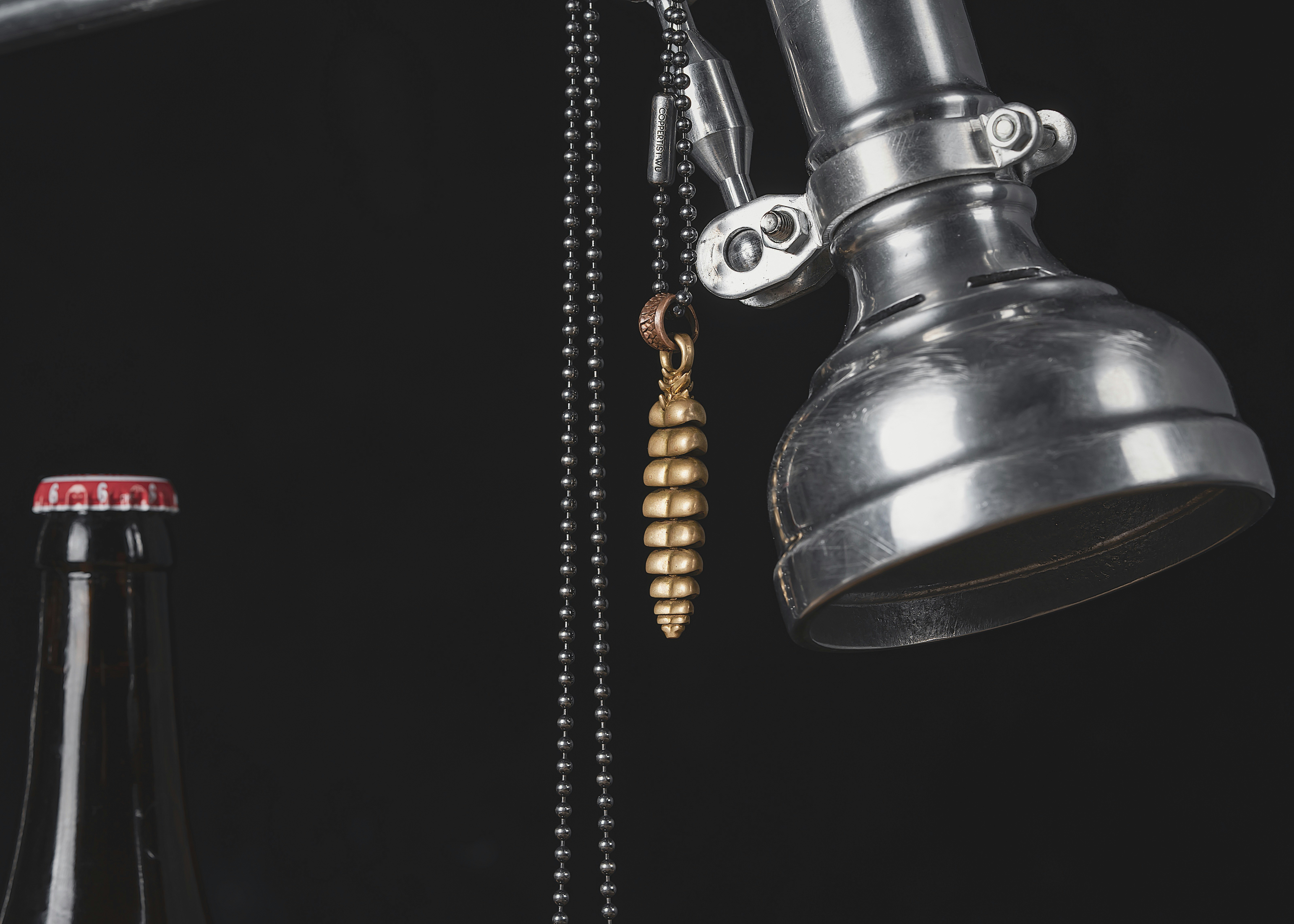 Noir Still Life: Chrome lamp, chain beads, and a brass pendant in shadow