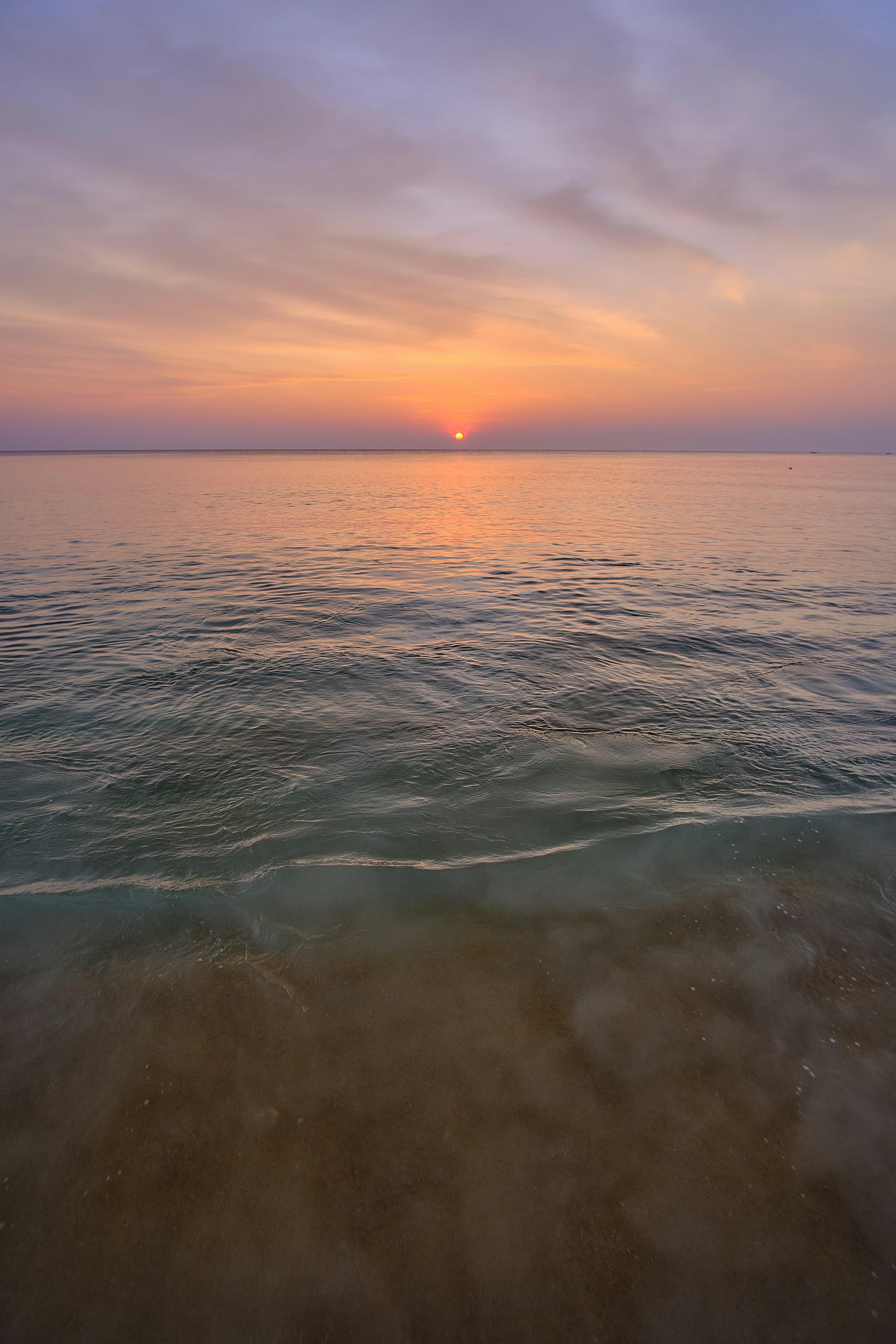 the sun is setting over the ocean on a cloudy day