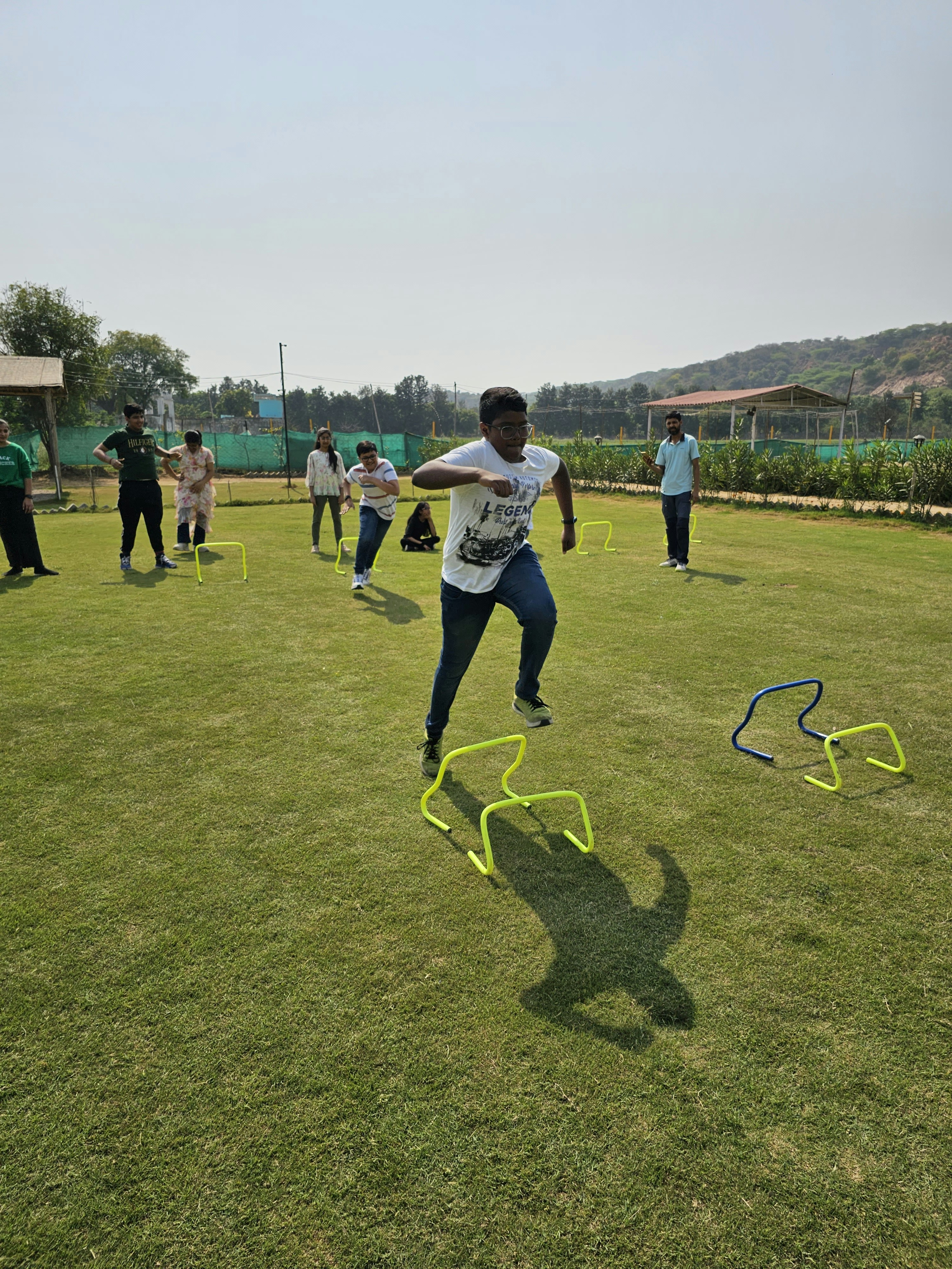 Midair Momentum: A Youth Leaps Over Hurdles on a Sunlit Field