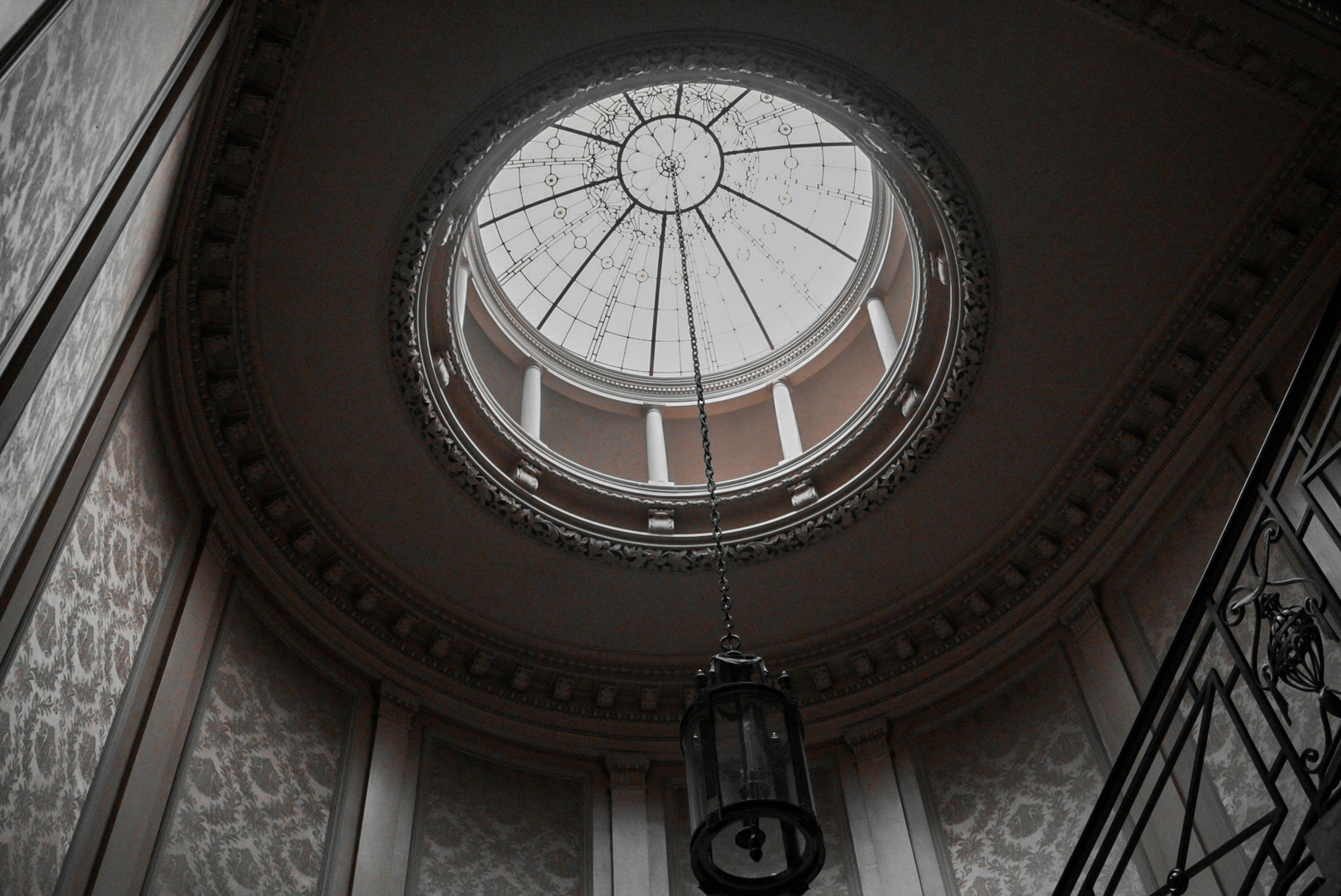 Ornate dome ceiling with intricate patterns and central chandelier in a dimly lit interior.
