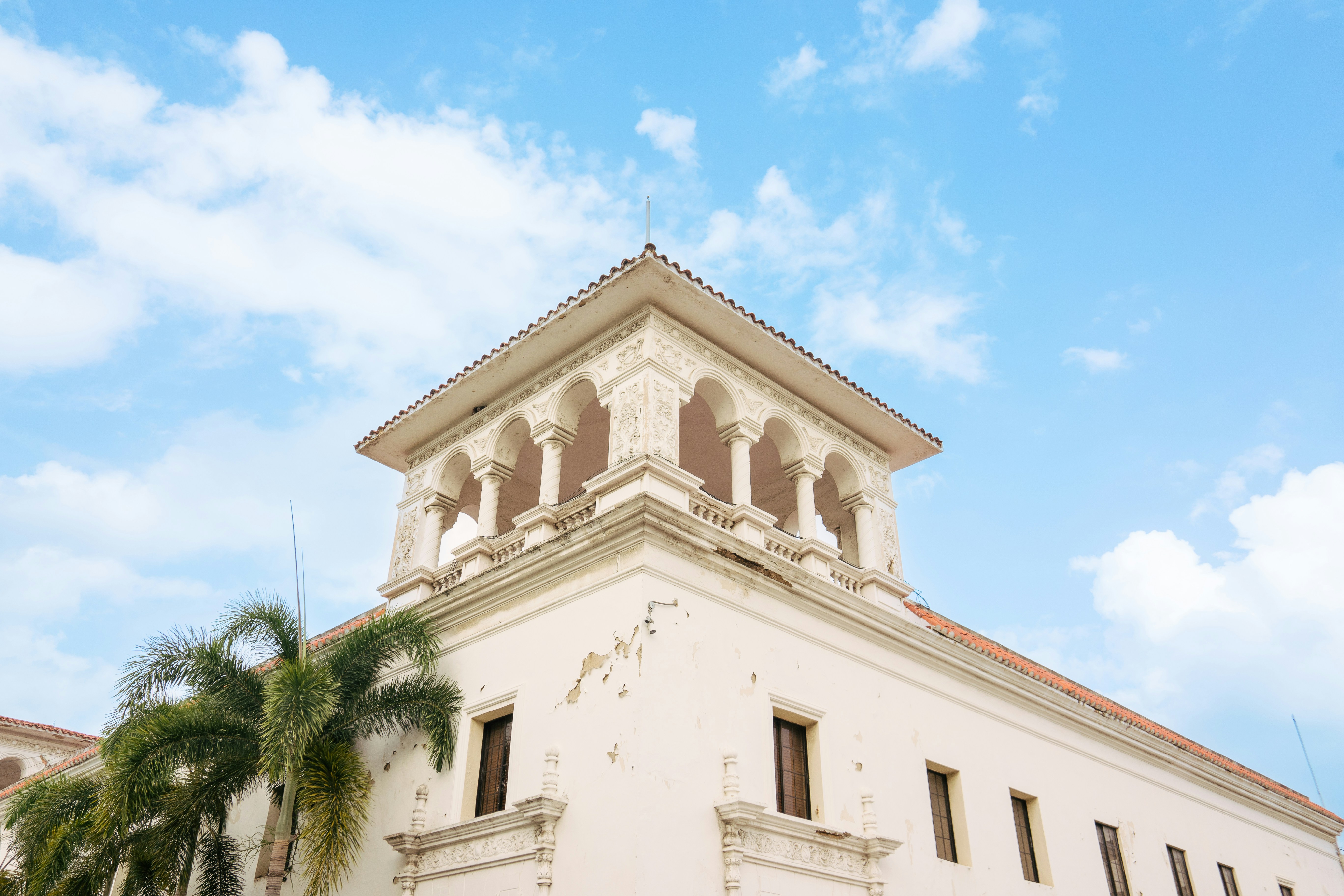 Historic building with arched windows and columns under a bright blue sky with scattered clouds.