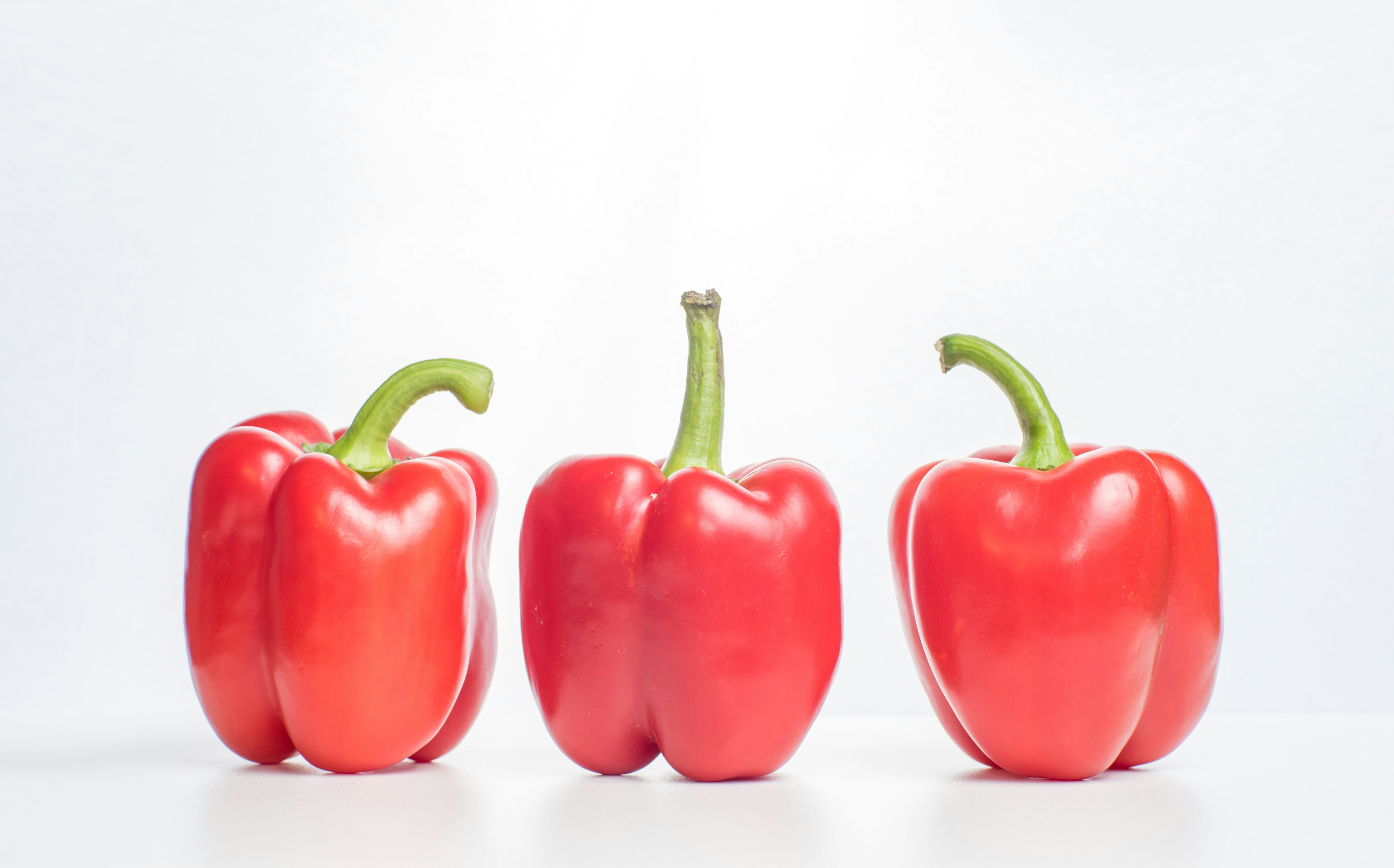 Three red peppers with green stems on a white surface photo – Free ...