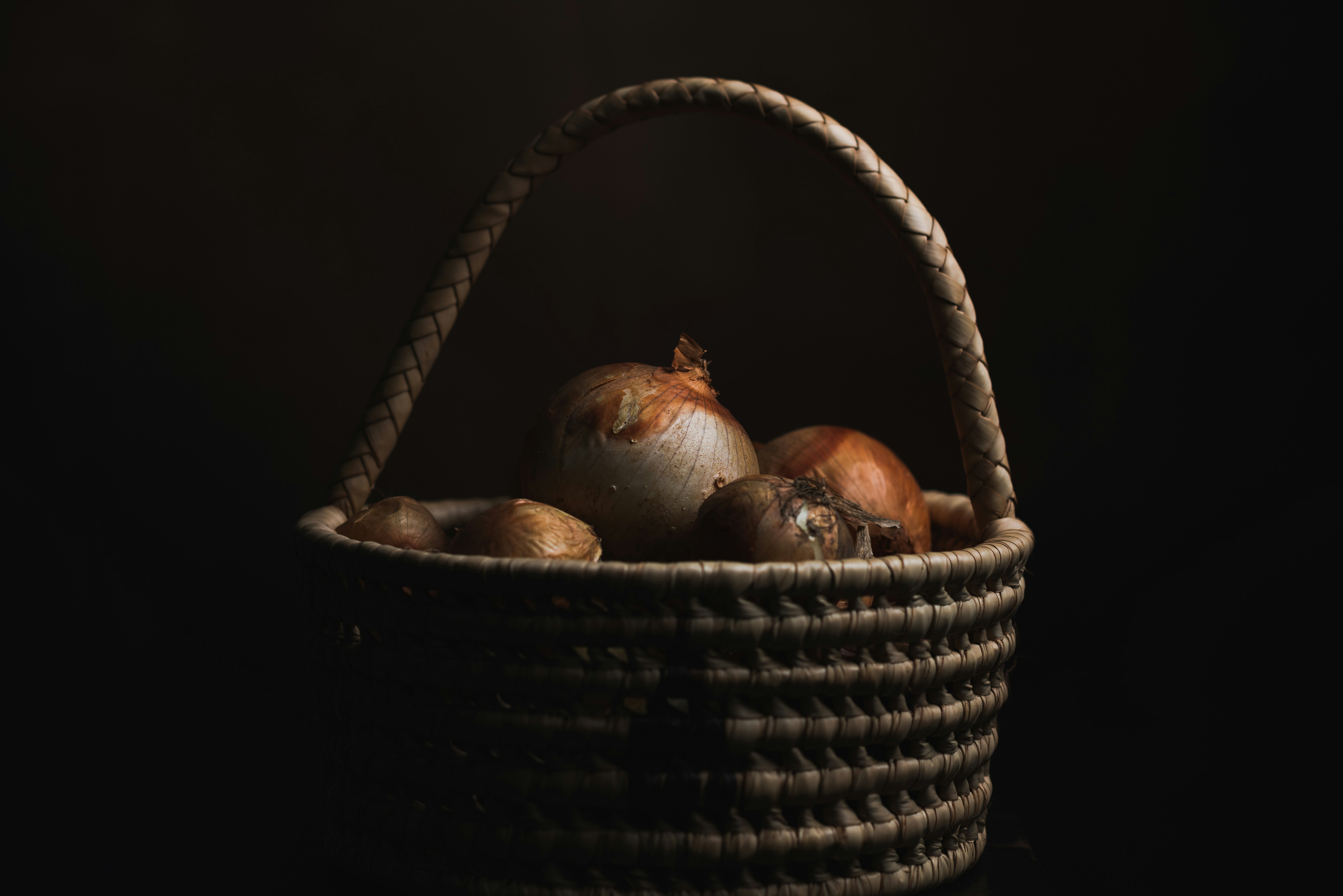 Woven basket filled with onions against a dark background.