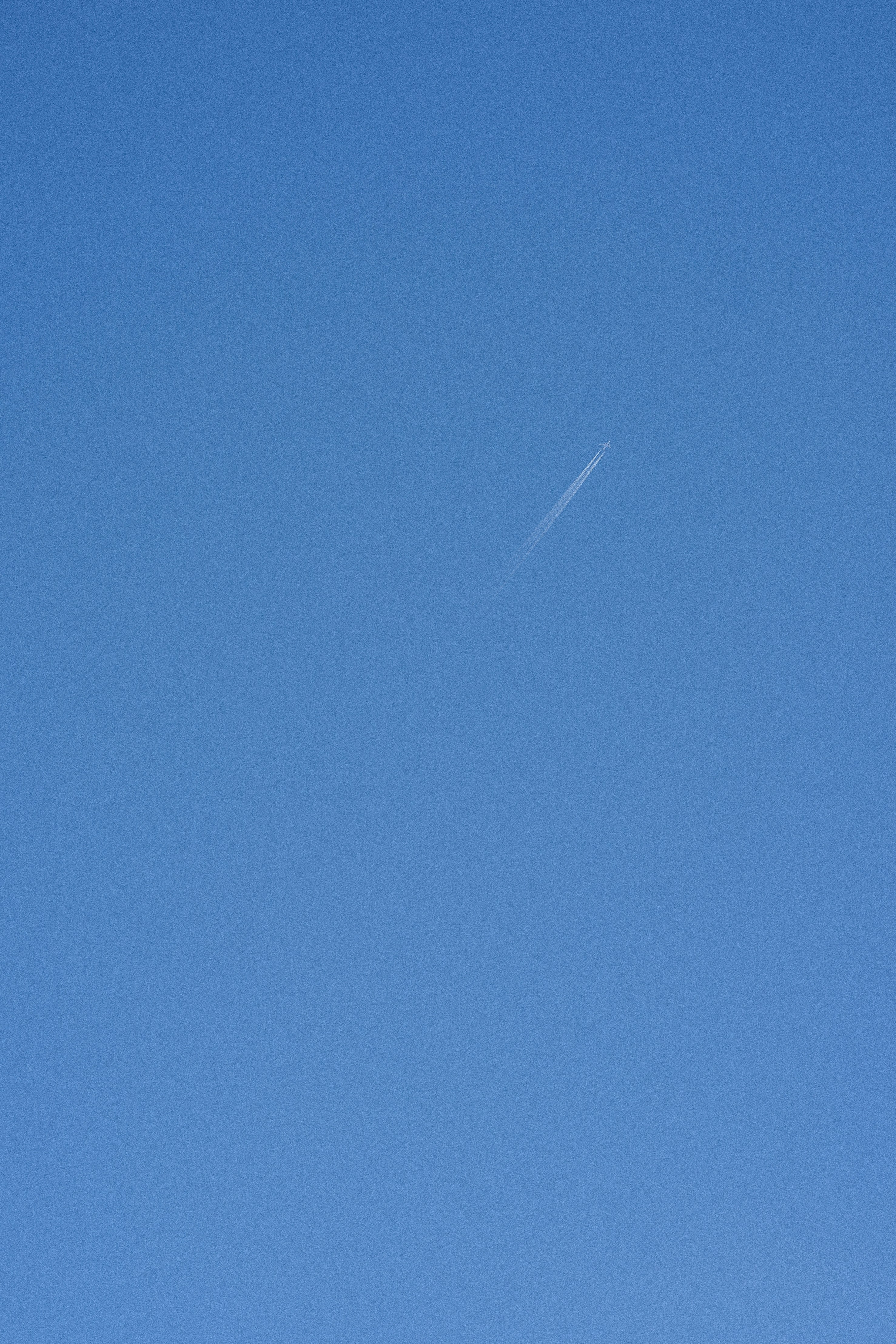 Jet leaving a faint vapor trail against a clear blue sky.