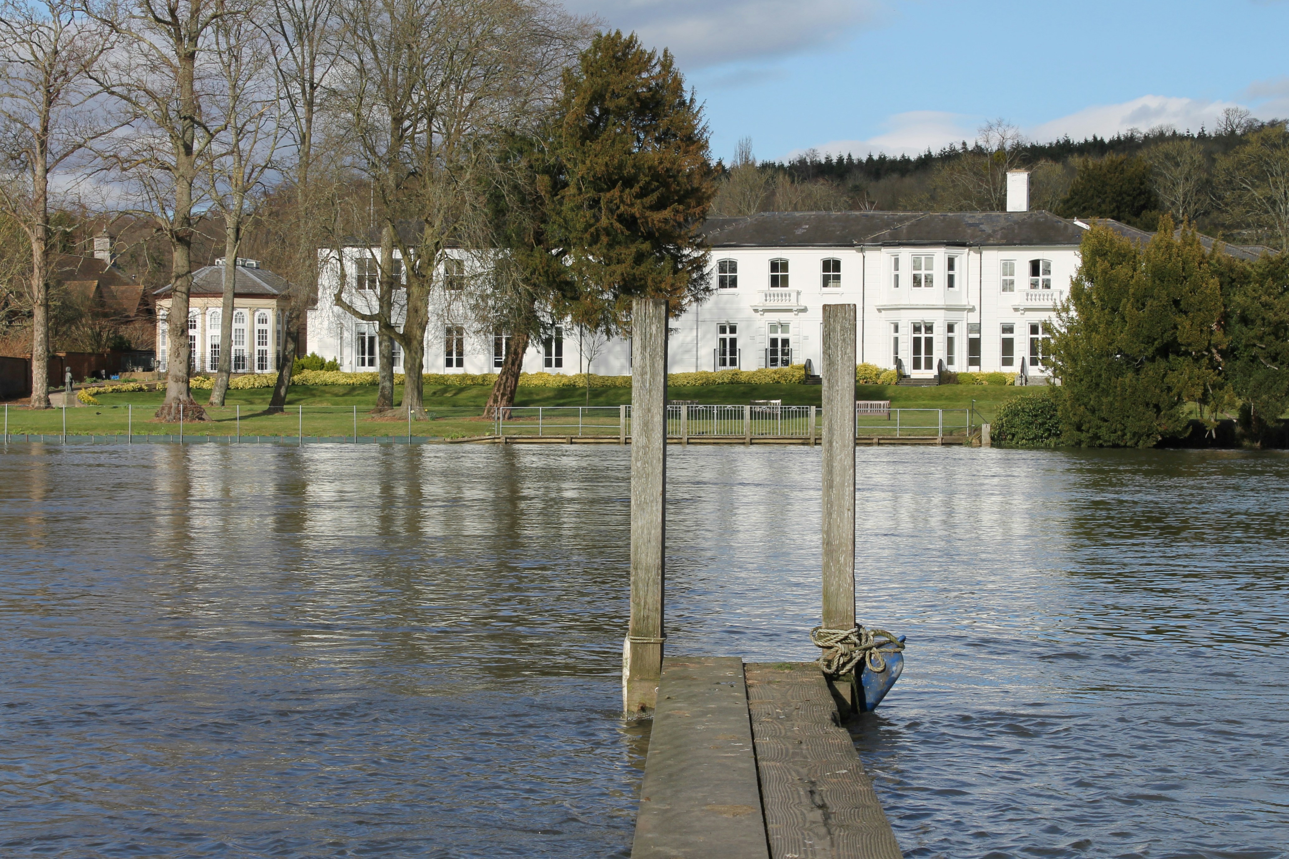 Charming white building reflected in calm waters, framed by lush greenery and a wooden dock leading into the scene.
