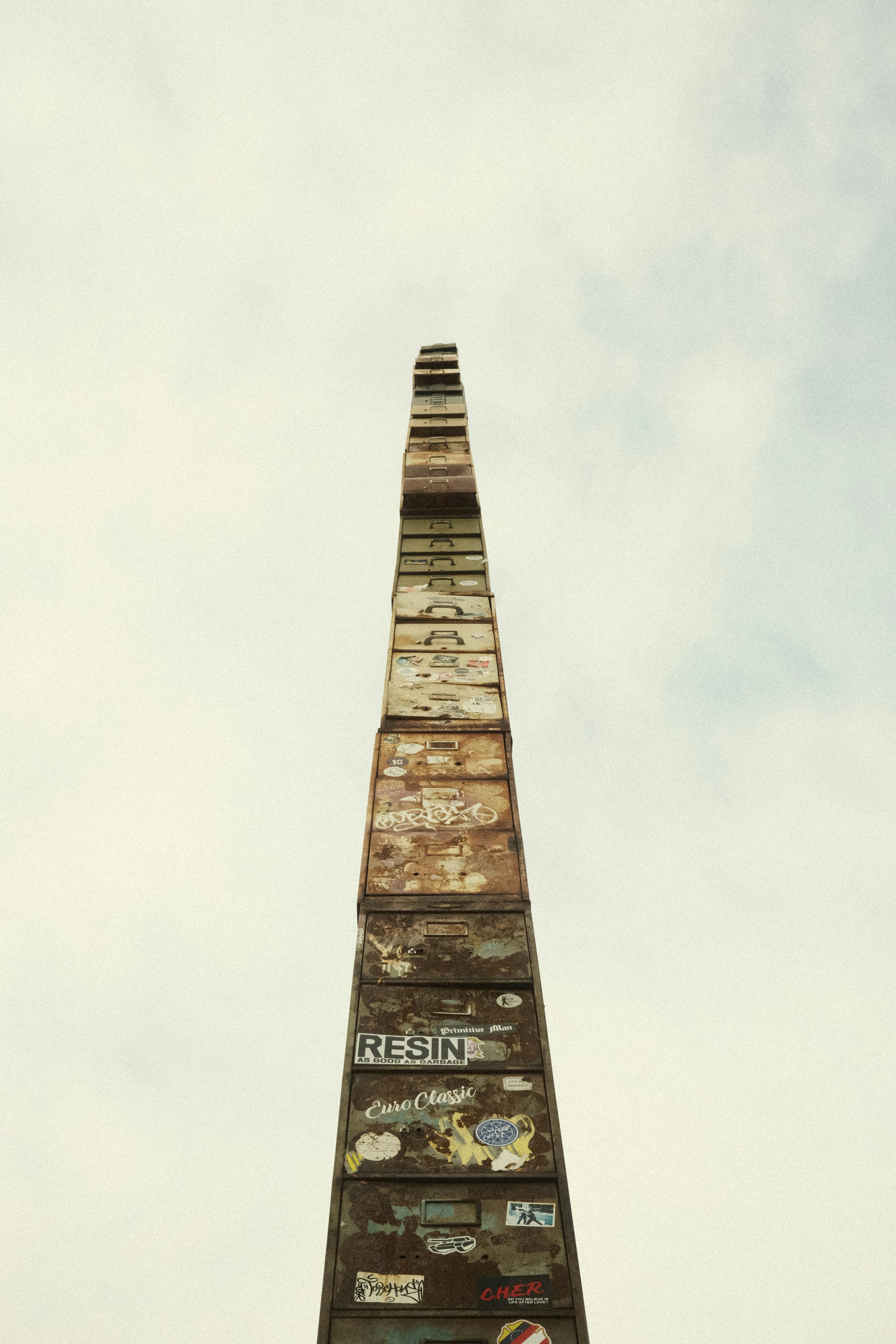 Rusted Column: A Tower of Weathered Boxes Ascending Toward a Pale Sky