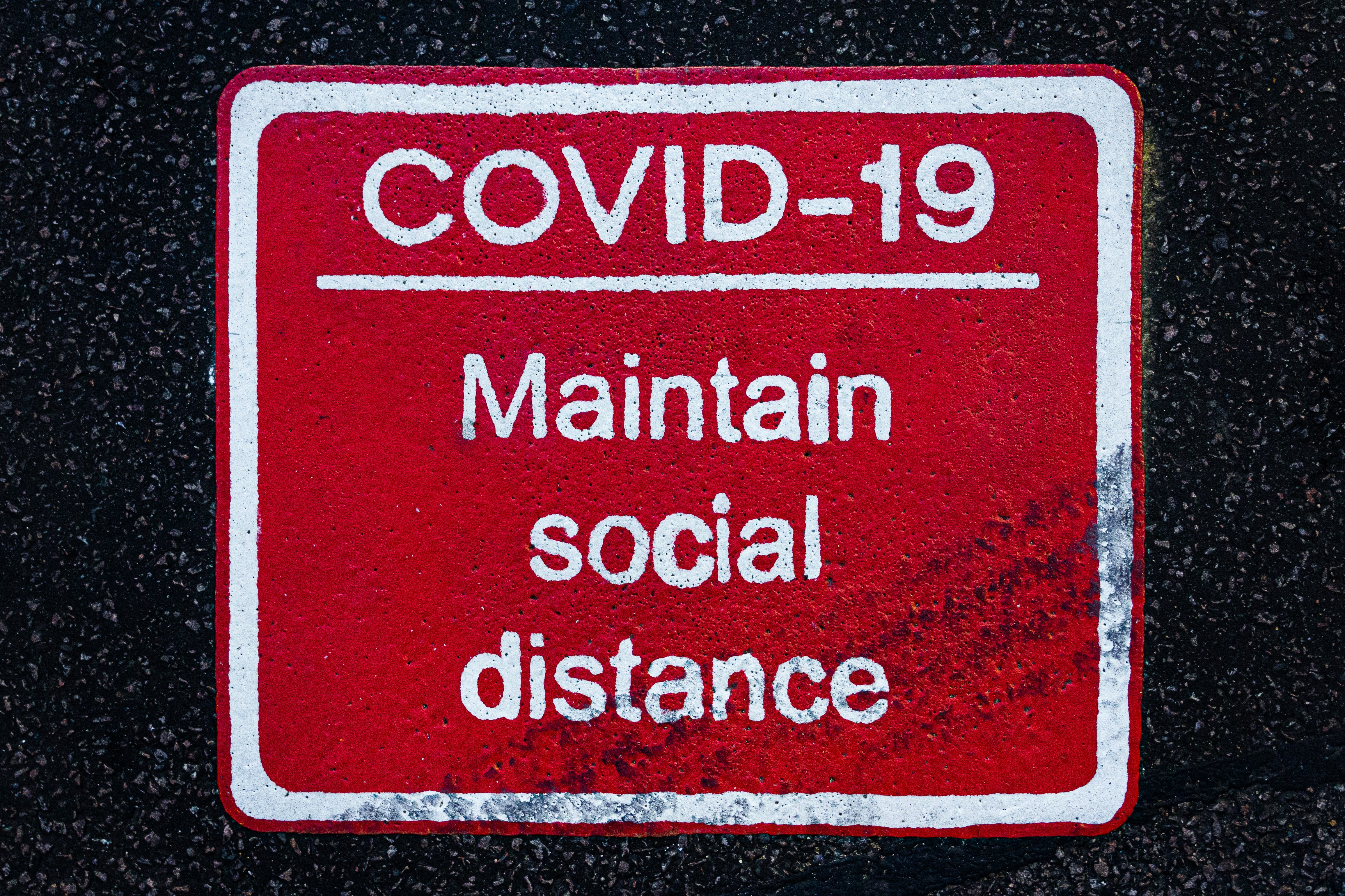 Red and white pavement sign instructing pedestrians to maintain social distance during the COVID-19 pandemic.