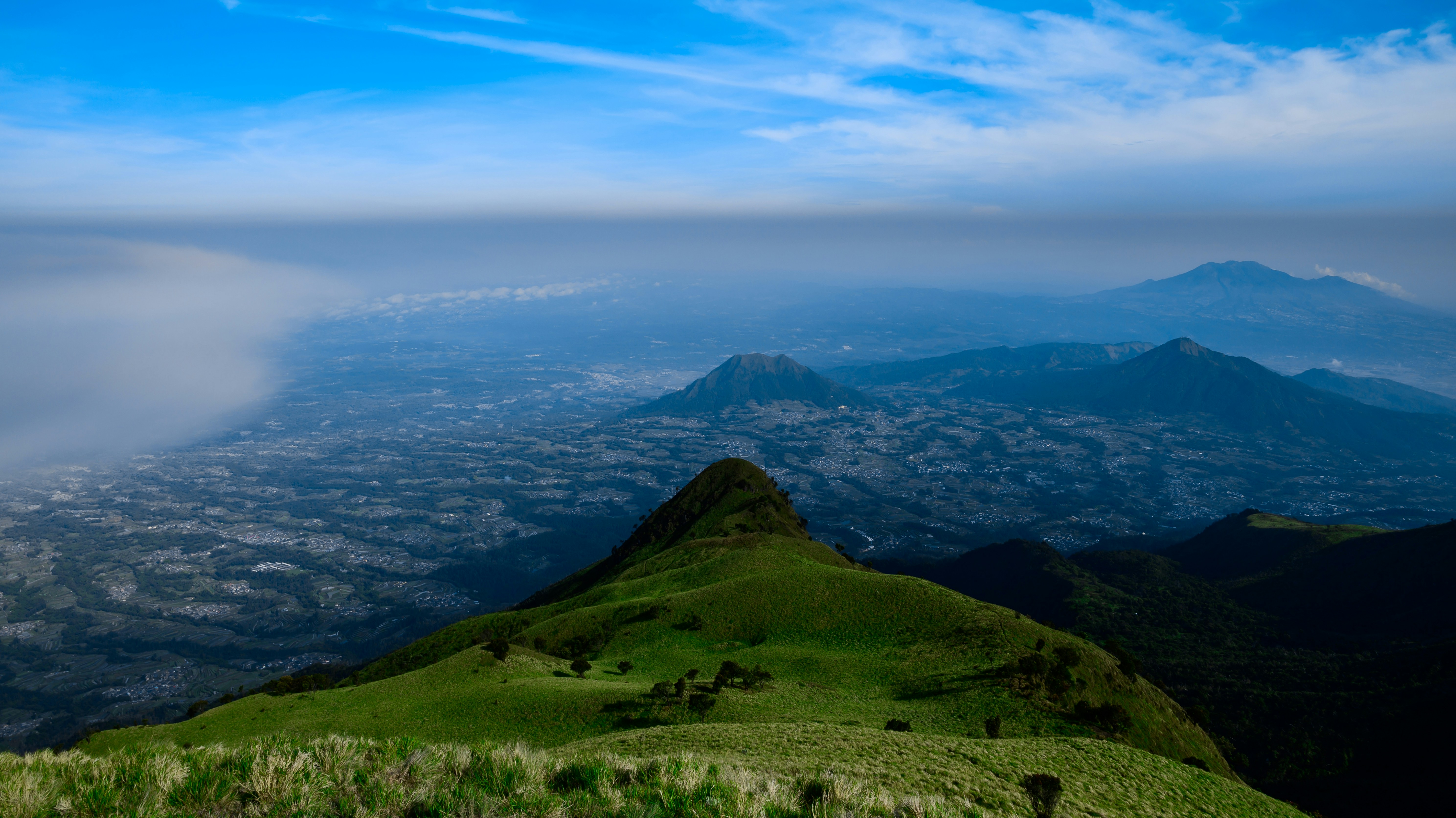 Rolling green hills stretch towards misty mountains under a vibrant blue sky.
