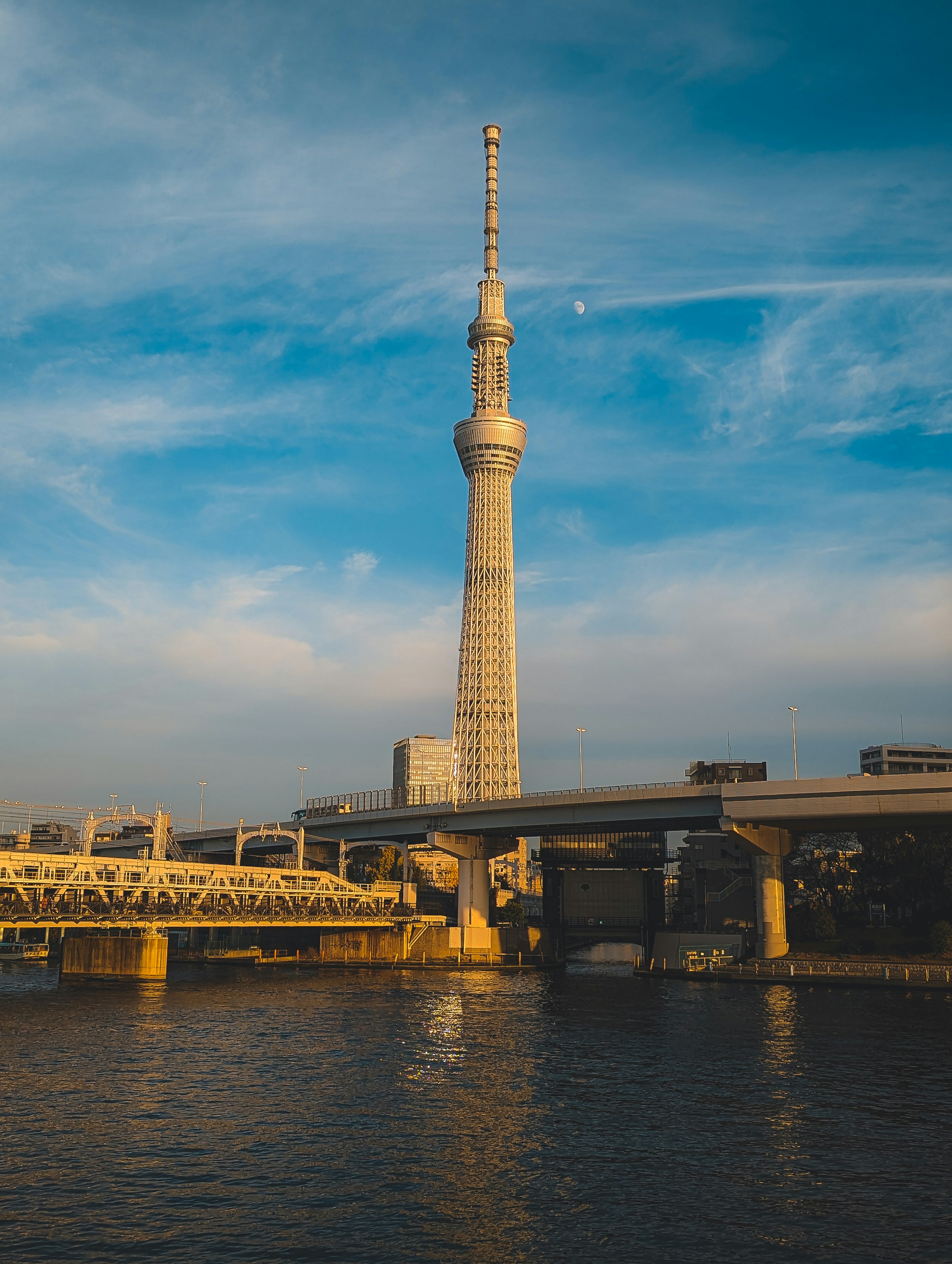 Tokyo Skytree rising majestically over the Sumida River, framed by urban architecture and a clear blue sky.