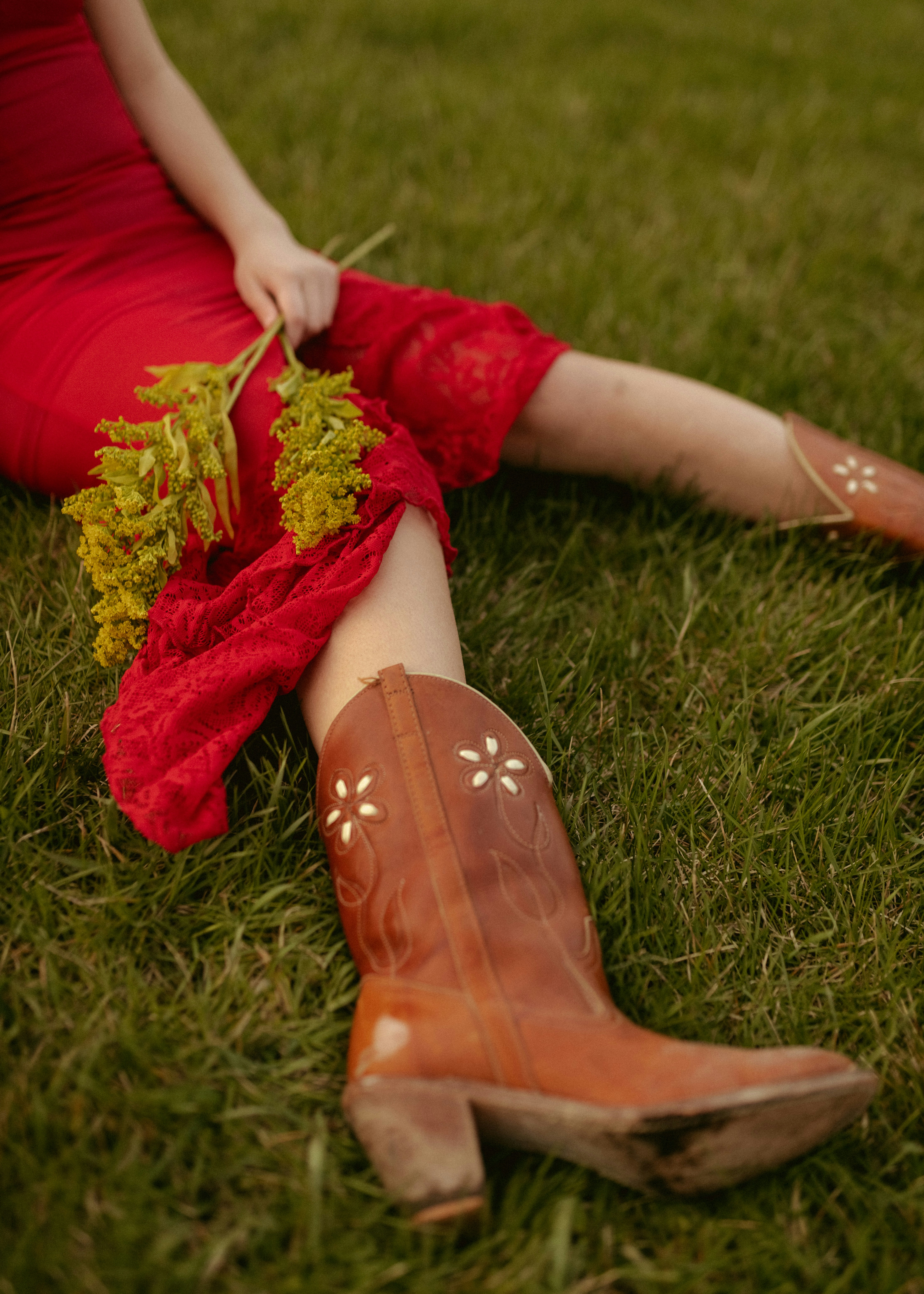 A woman in a red dress holding a bouquet of green flowers while seated on grass, showcasing a blend of fashion and nature.