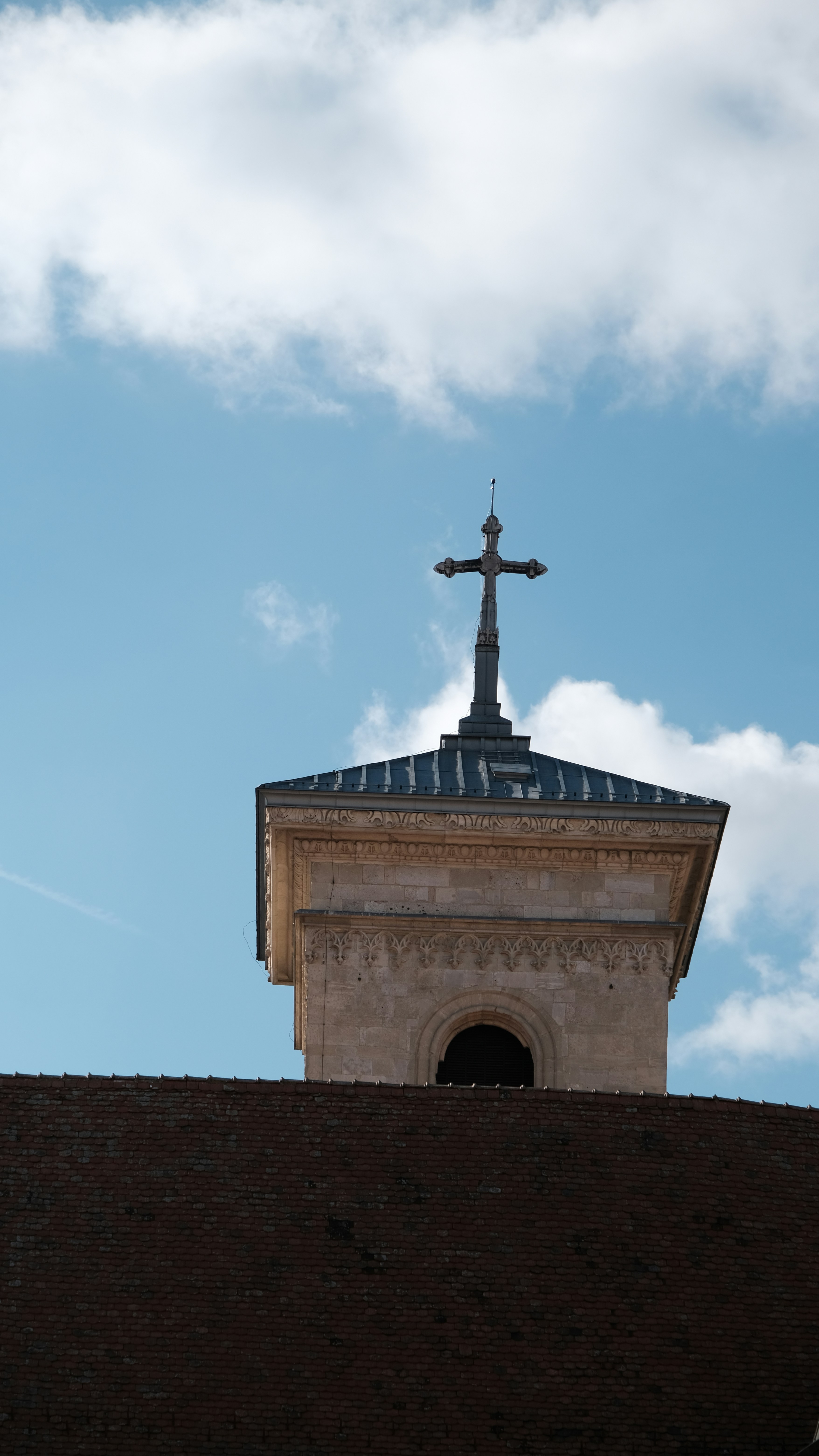 Catholic church steeple over the roof. | a cross on top of a building with a sky background
