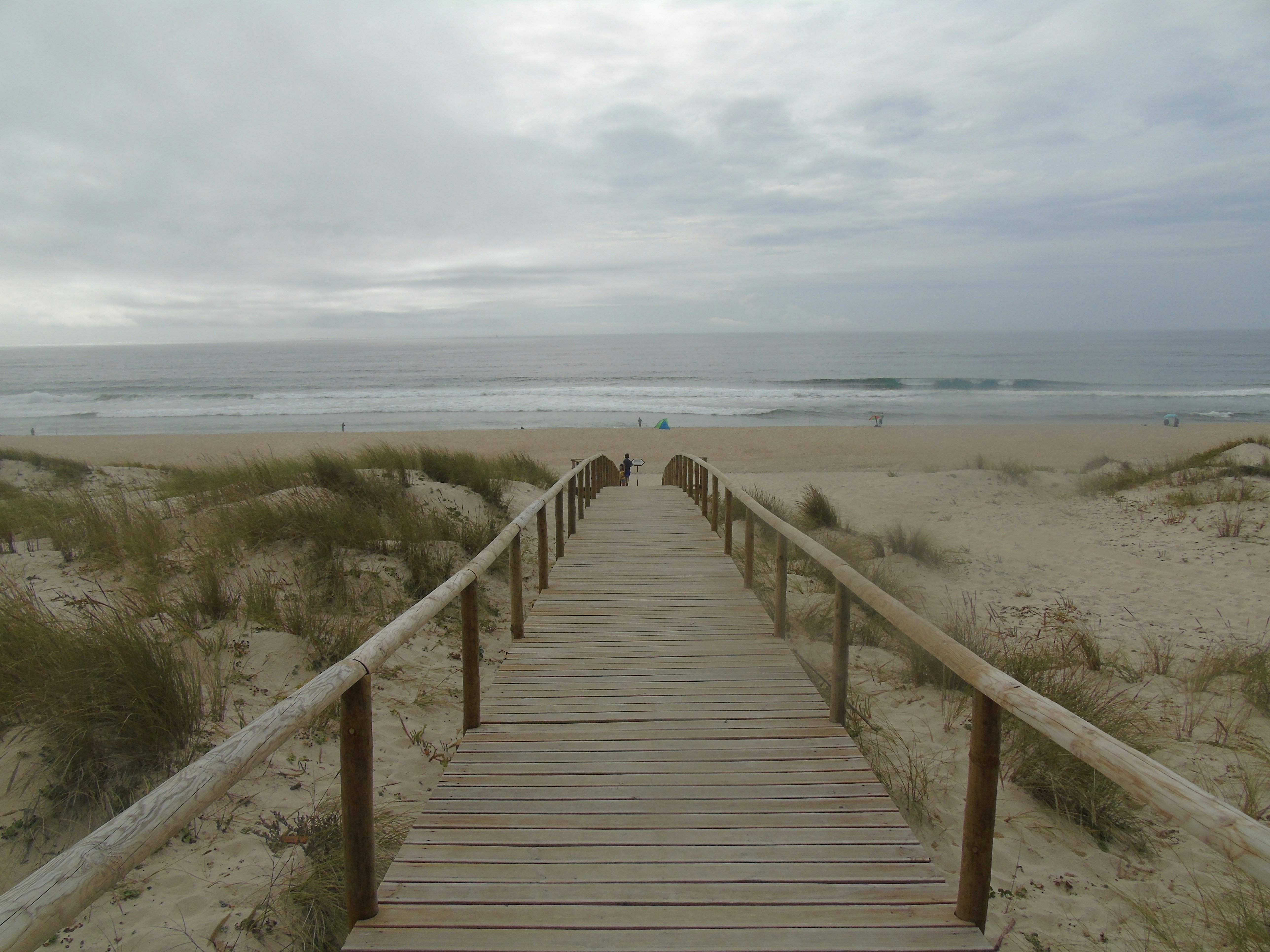 Wooden walkway leading through sandy dunes to a cloudy ocean horizon.