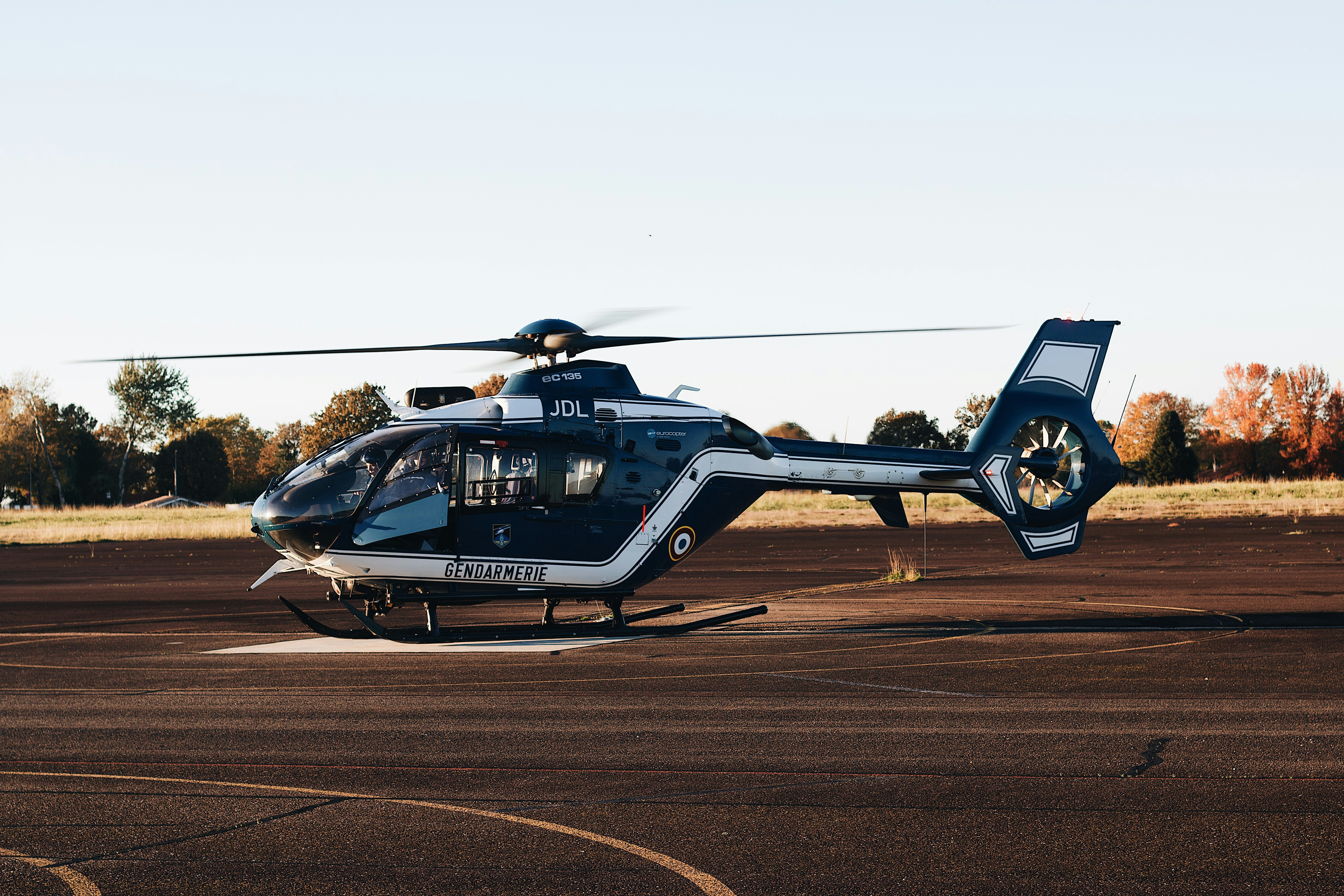 Helicopter positioned on a sunlit tarmac with trees and clear sky in the background.