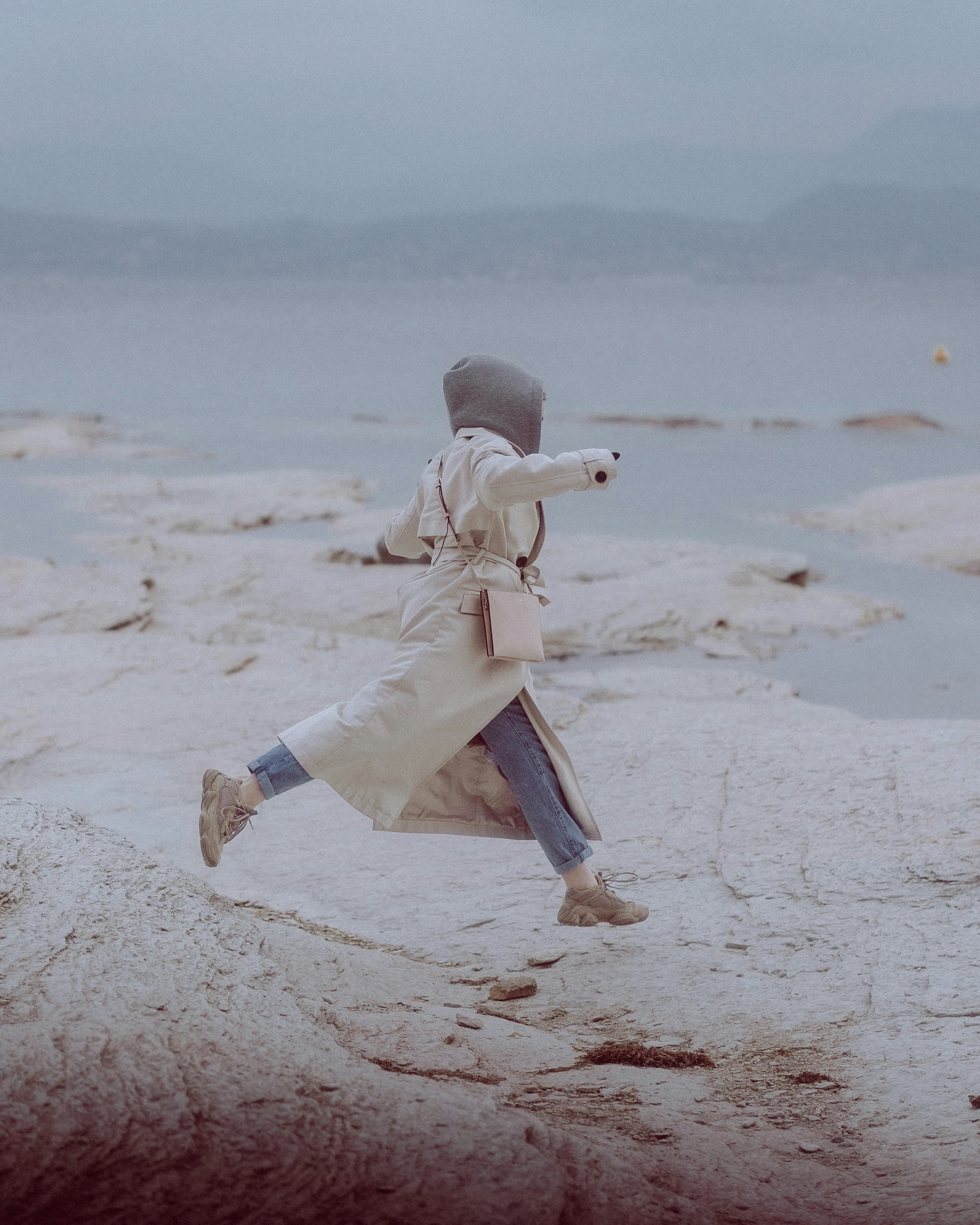A Quiet Leap: Child in a Trench Coat Crossing a Misty Shore
