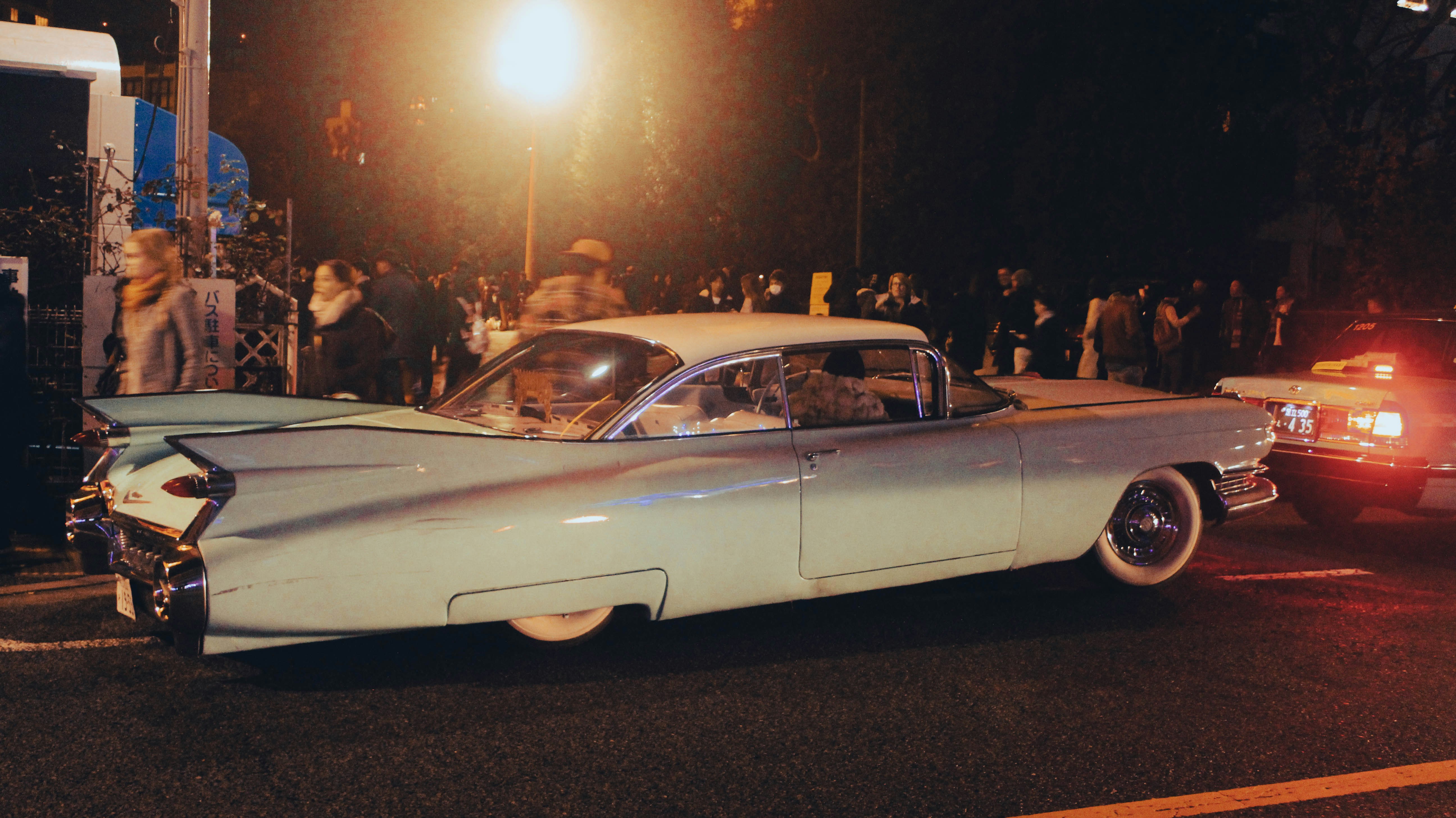 Moonlit Classic: Mint-blue 1950s vintage sedan at a neon-lit street gathering