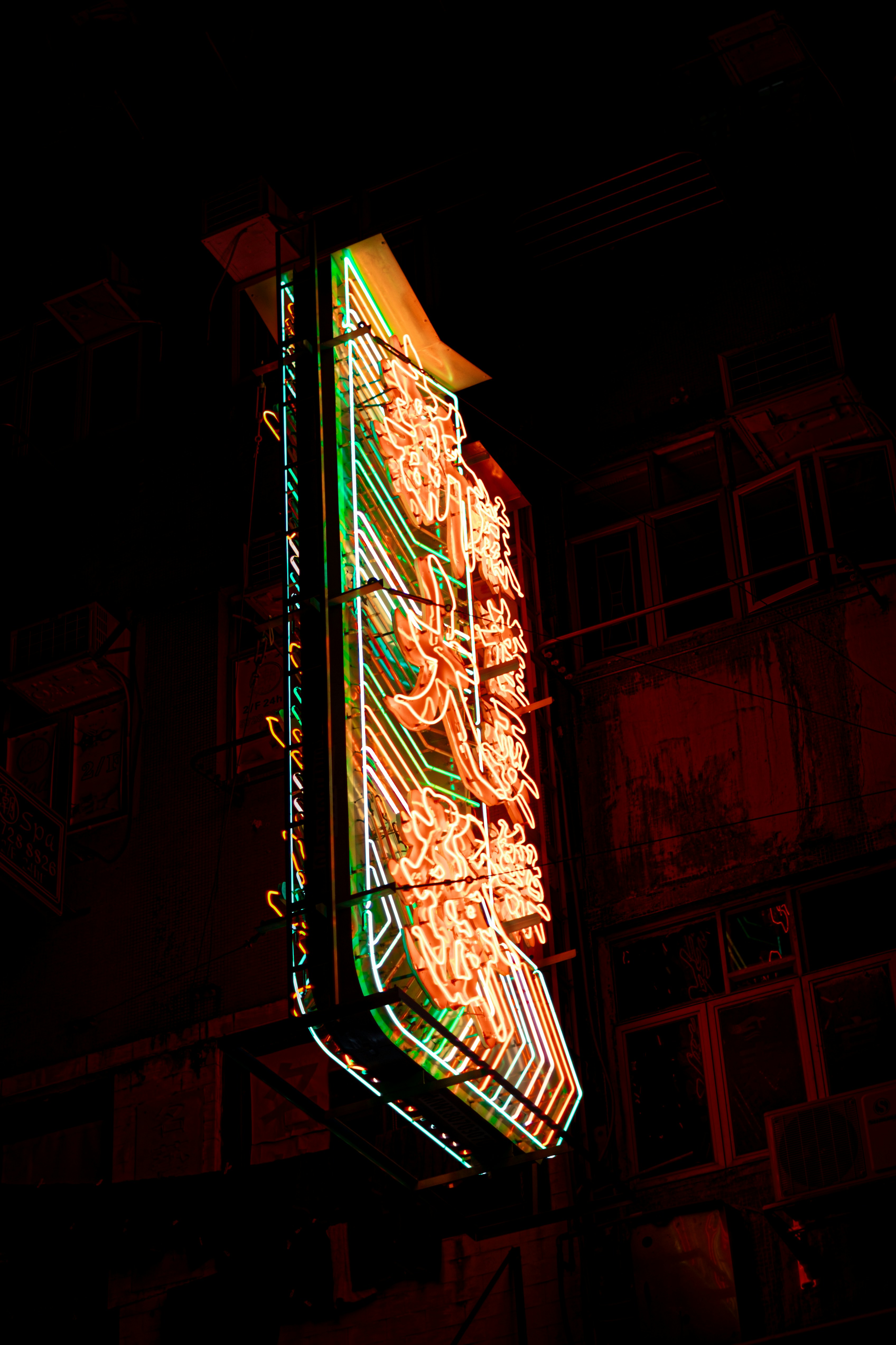 Pulse of the Night: Vertical Neon Sign Illuminates a Weathered Urban Facade