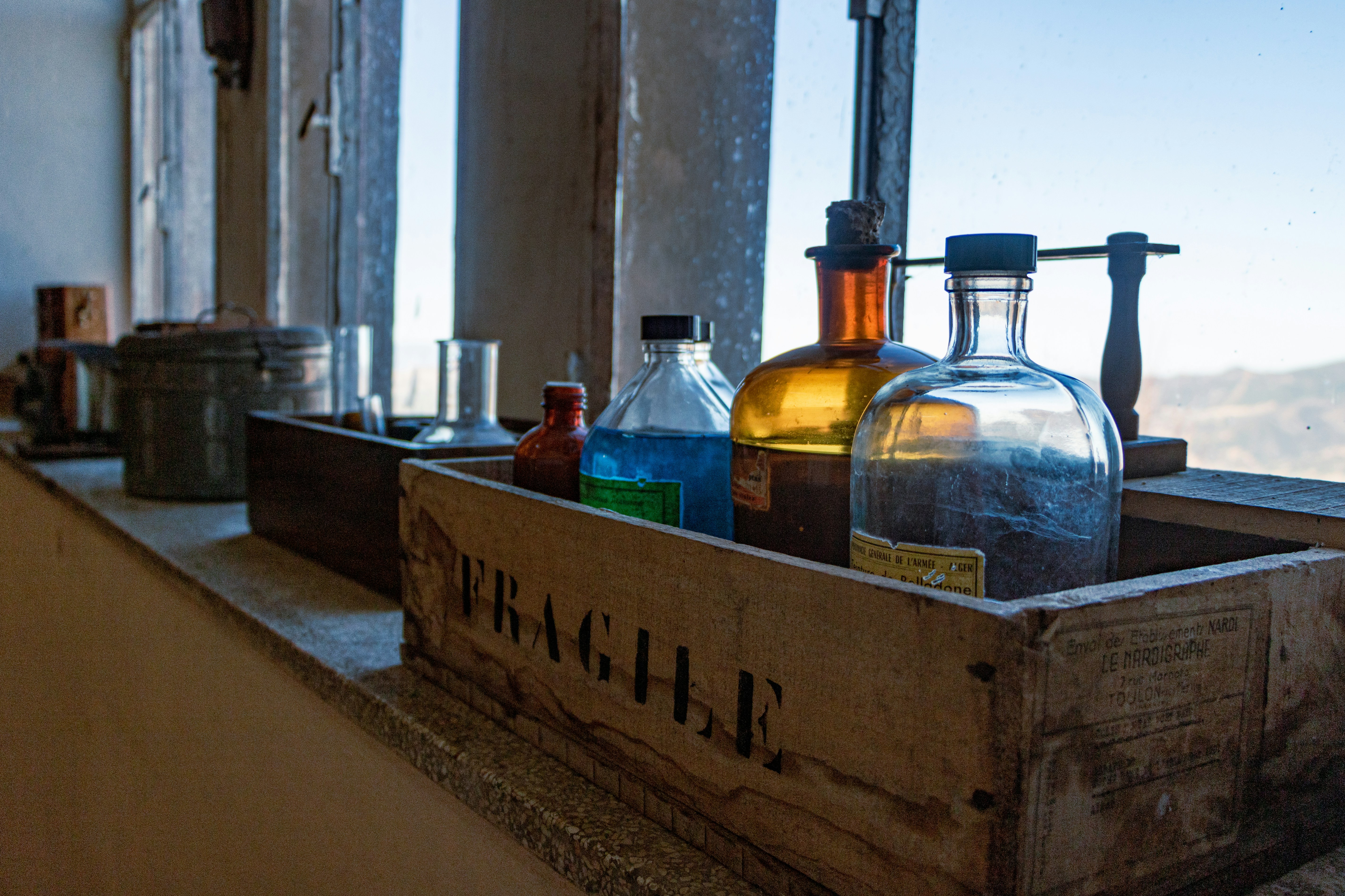Collection of vintage glass bottles and jars arranged on a windowsill, illuminated by natural light filtering through the glass. 