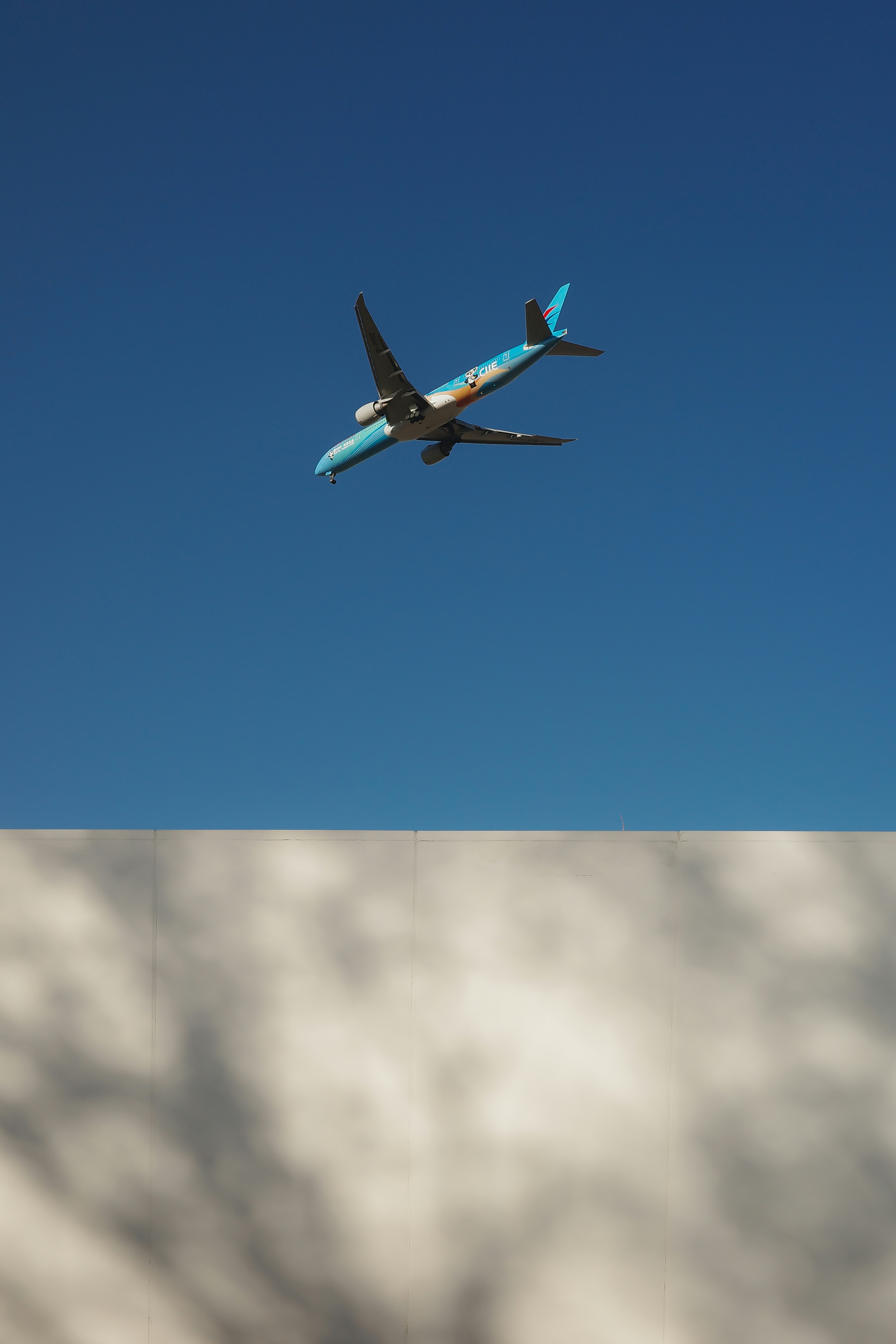 A commercial airplane soaring through a clear blue sky, with a stark white surface below creating a contrasting backdrop.