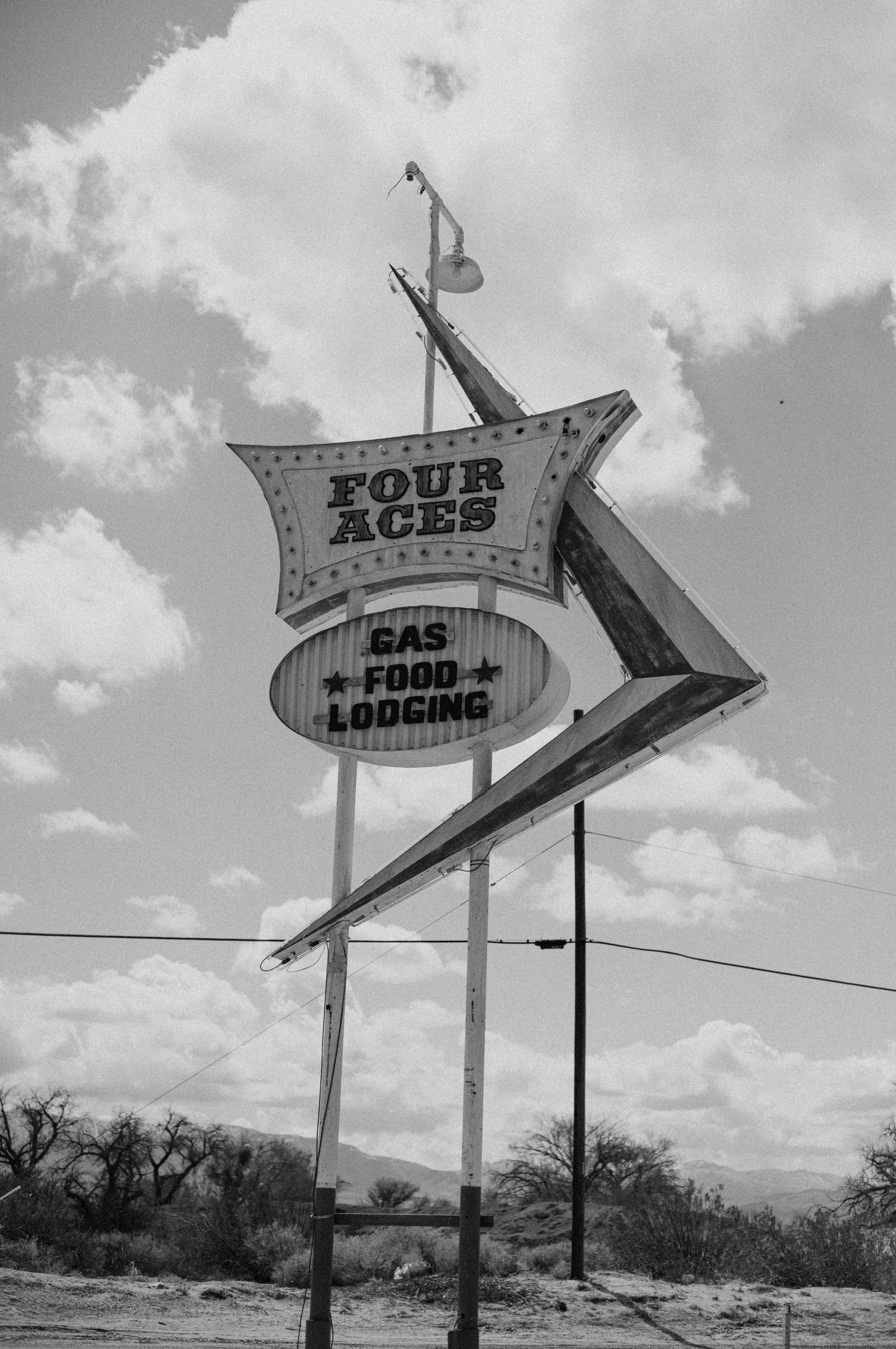 Vintage motel sign for Four Aces announces gas, food, and lodging against a windy desert sky.