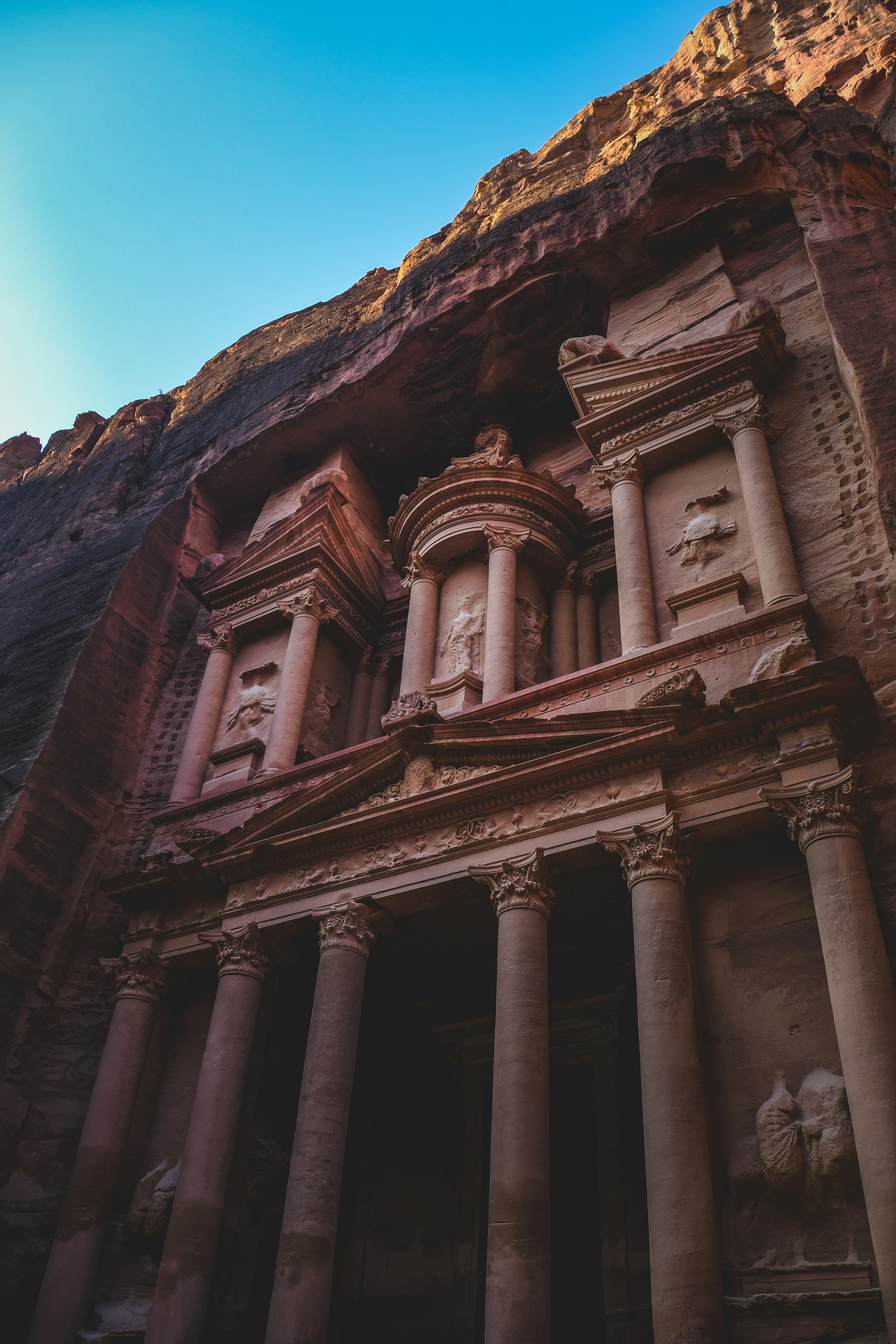 The Treasury of Petra, an architectural marvel carved into rose-red cliffs, showcases intricate columns and sculptures under a clear blue sky.