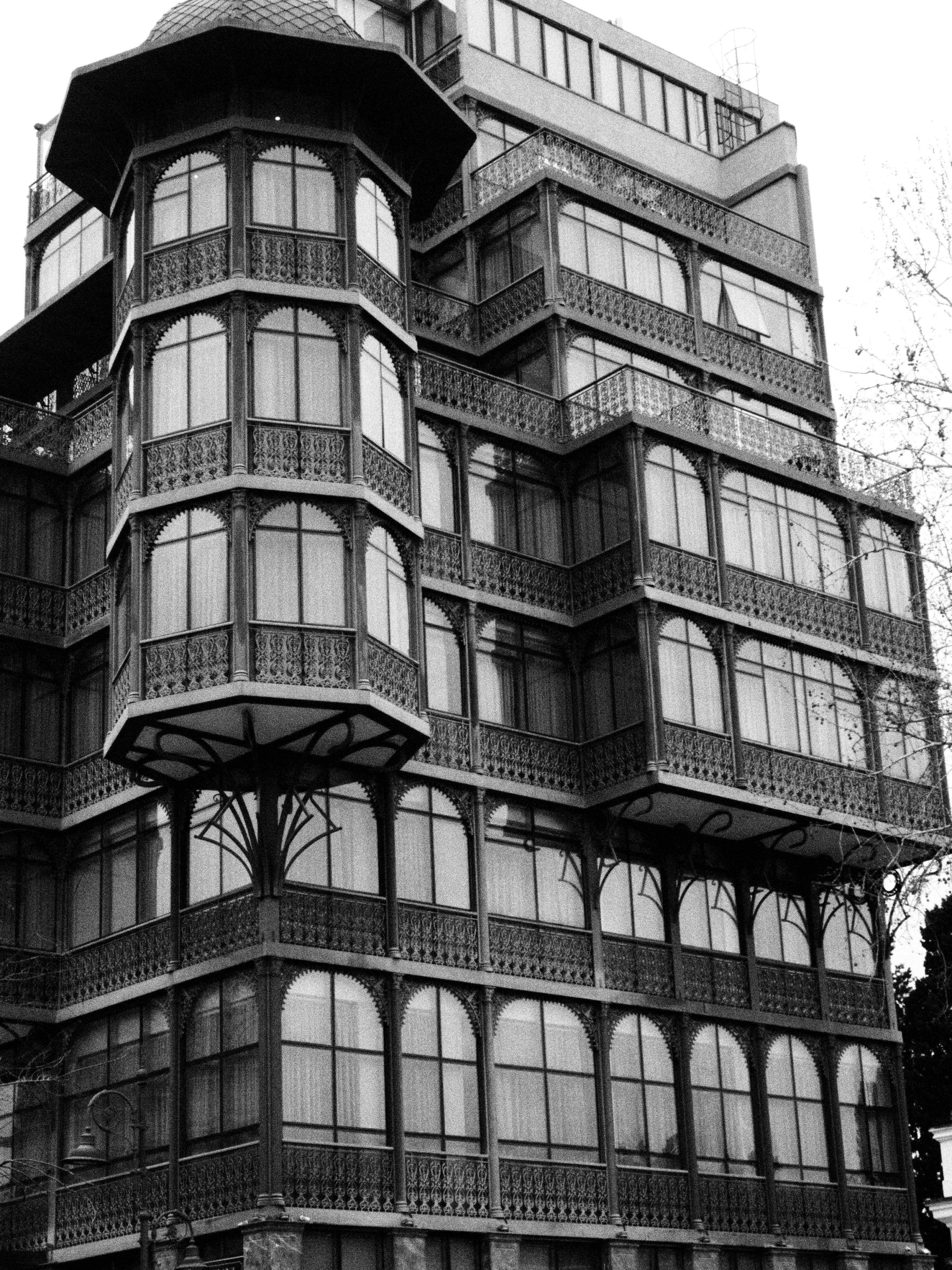 Monochrome photograph of a multi-story building with ornate curved bay windows and intricate iron lattice balconies.