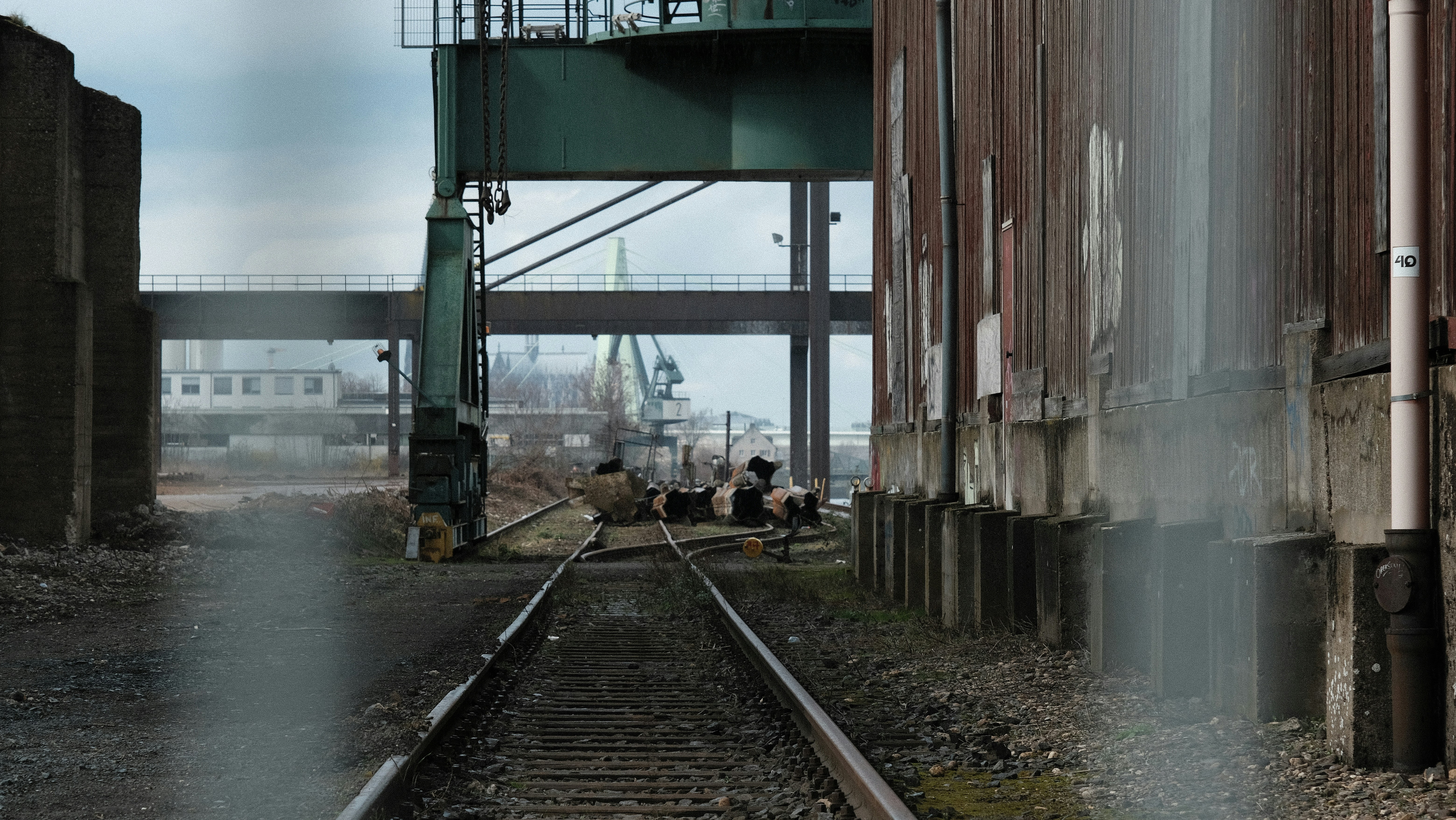 Tracks Converge Under a Green Gantry Toward a Distant Crew