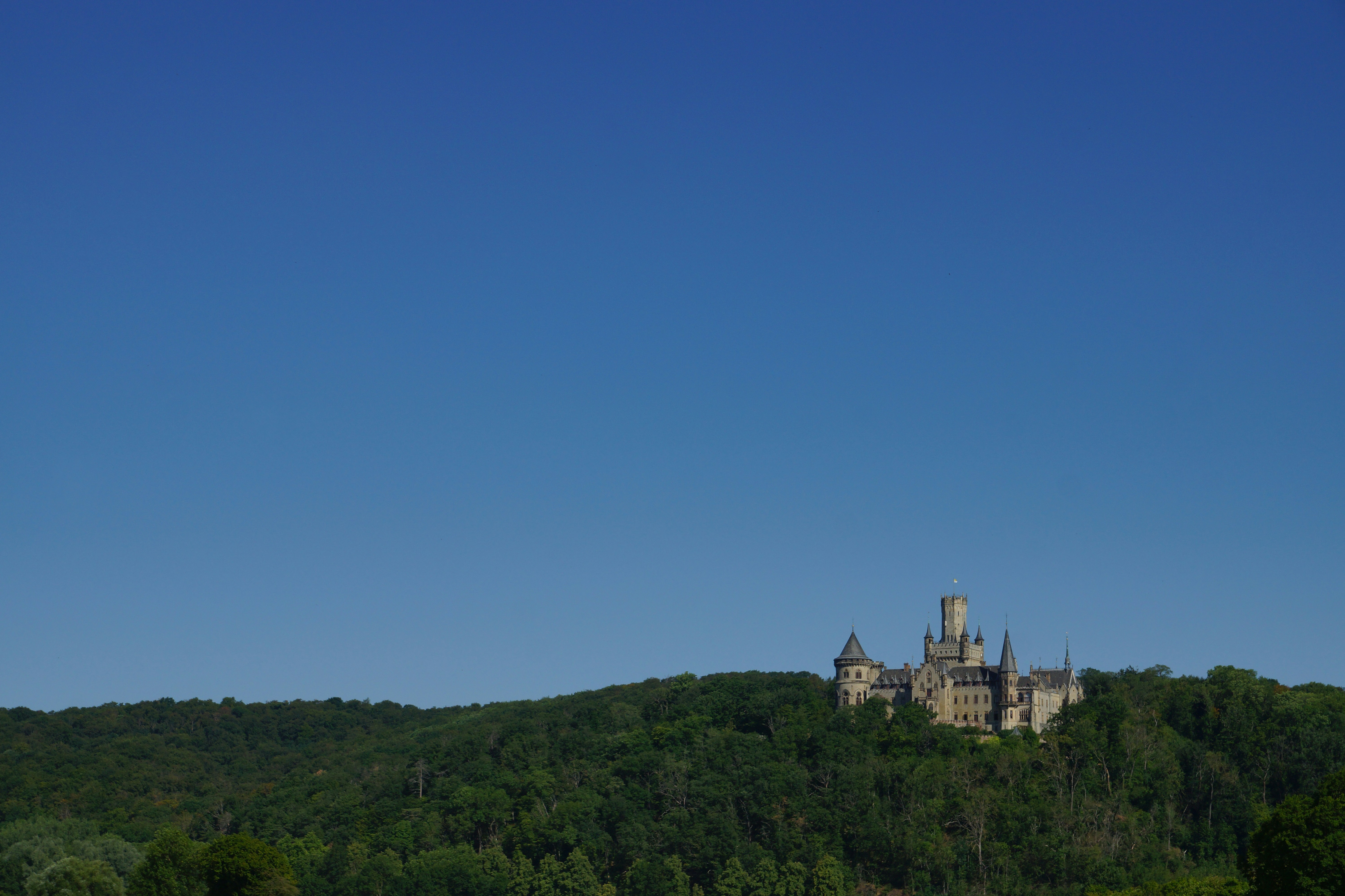 Marienburg Castle perched on a lush green hill under a clear blue sky.